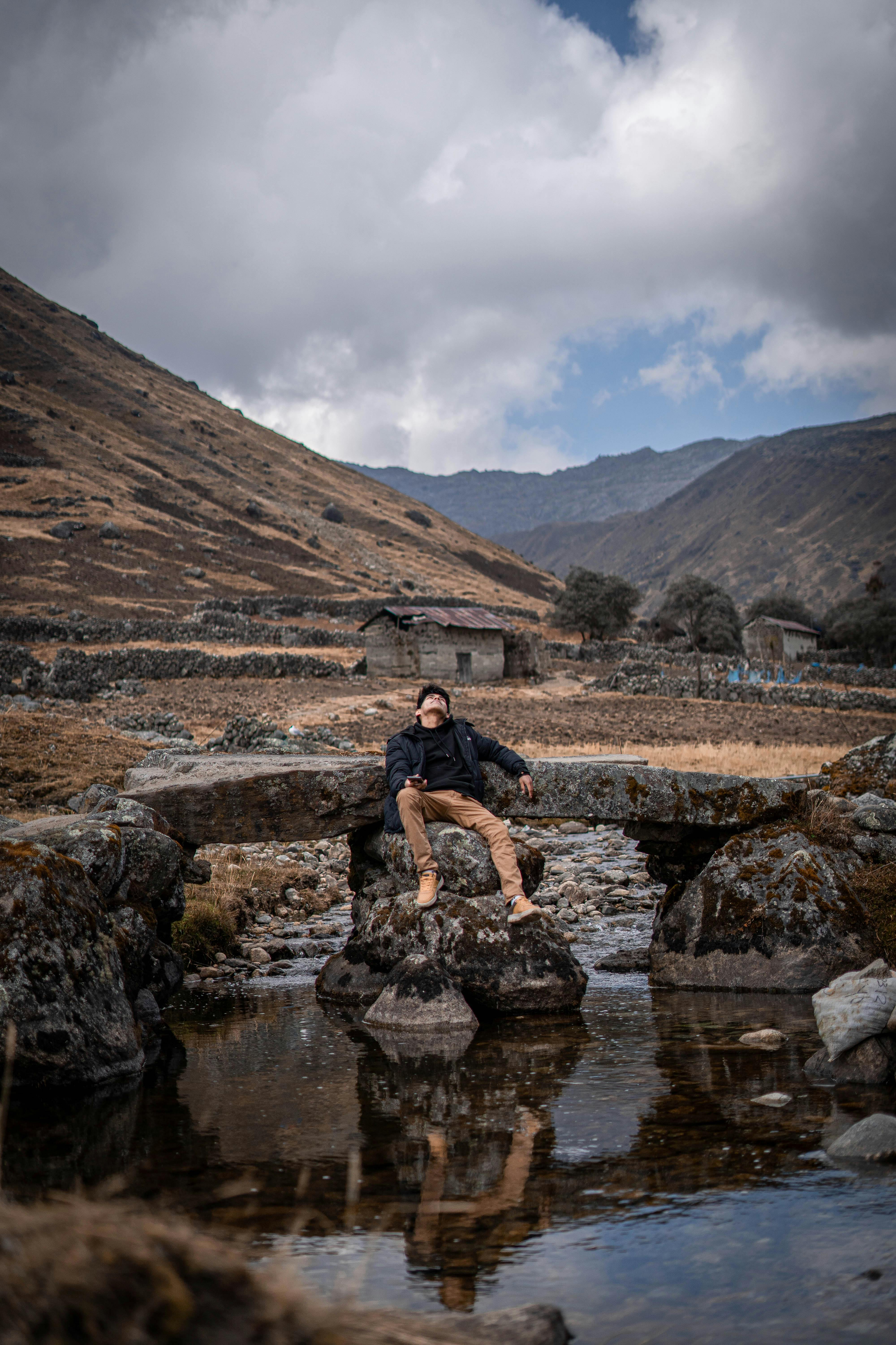 Man Sitting on Stones Supporting a Crumbling Footbridge · Free Stock Photo