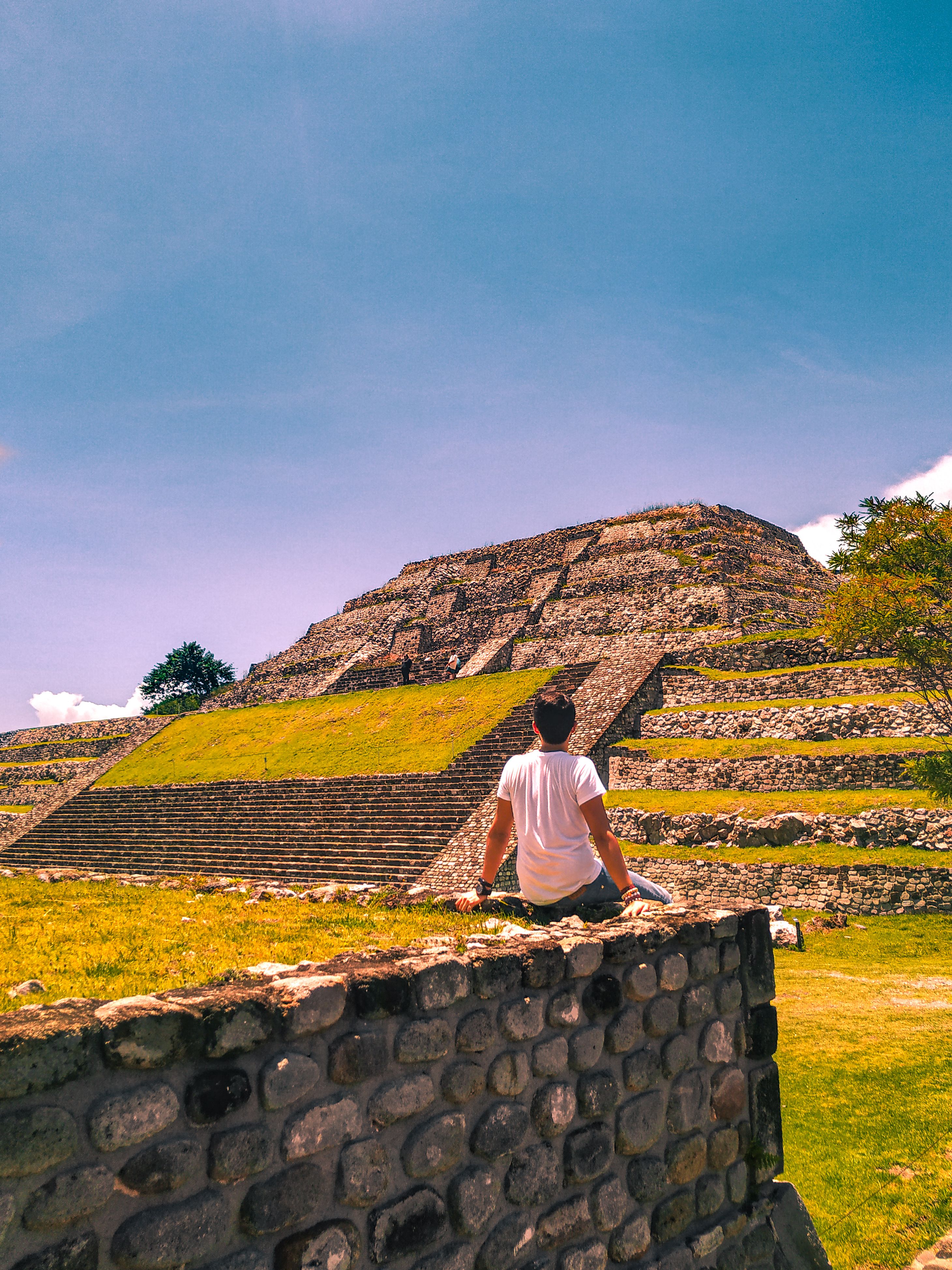 Man Sitting on Stone Wall with Ancient Pyramid behind · Free Stock Photo