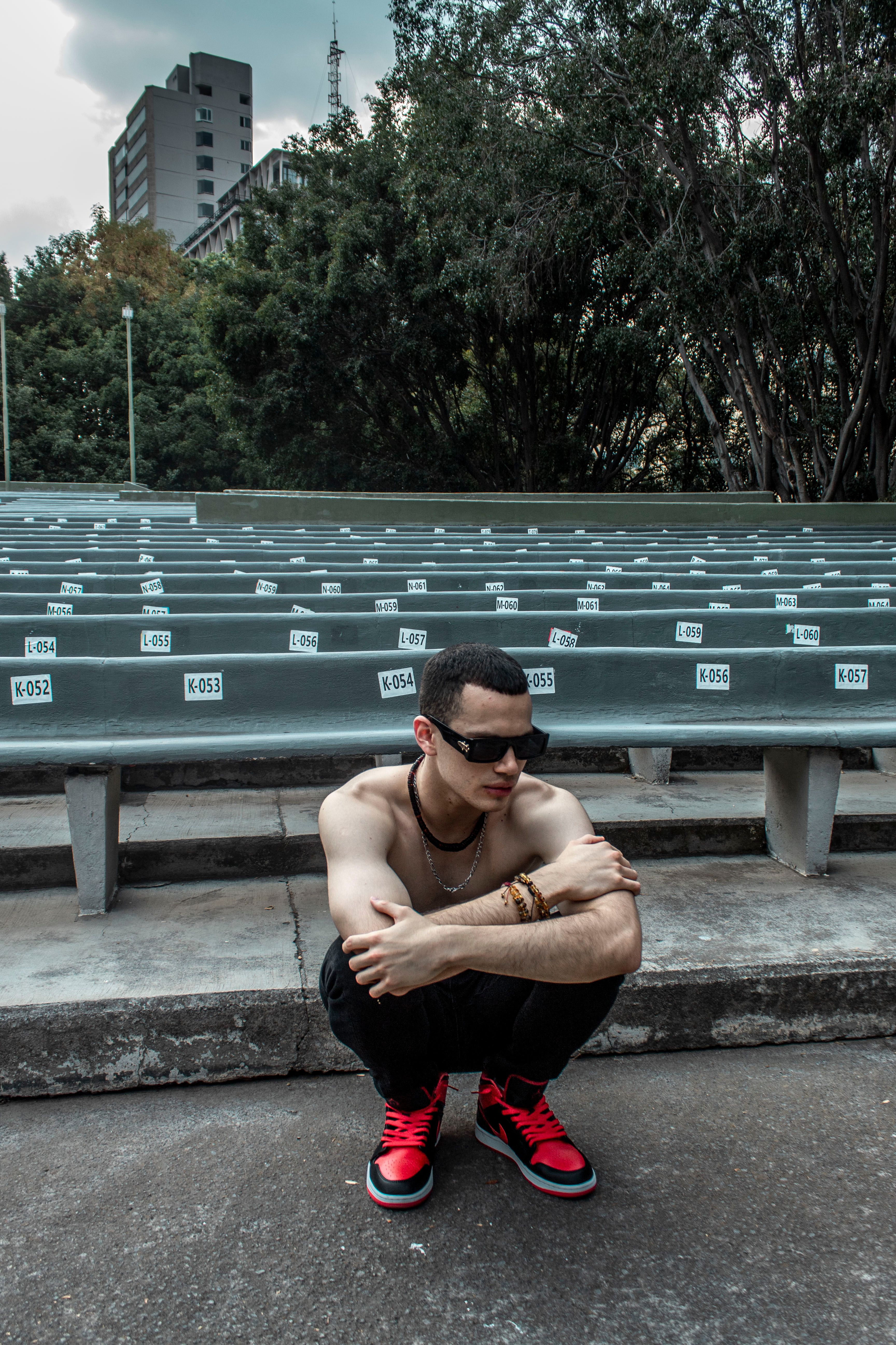 Shirtless Man Crouching in Black and Red Trainers by Seats in Park ...