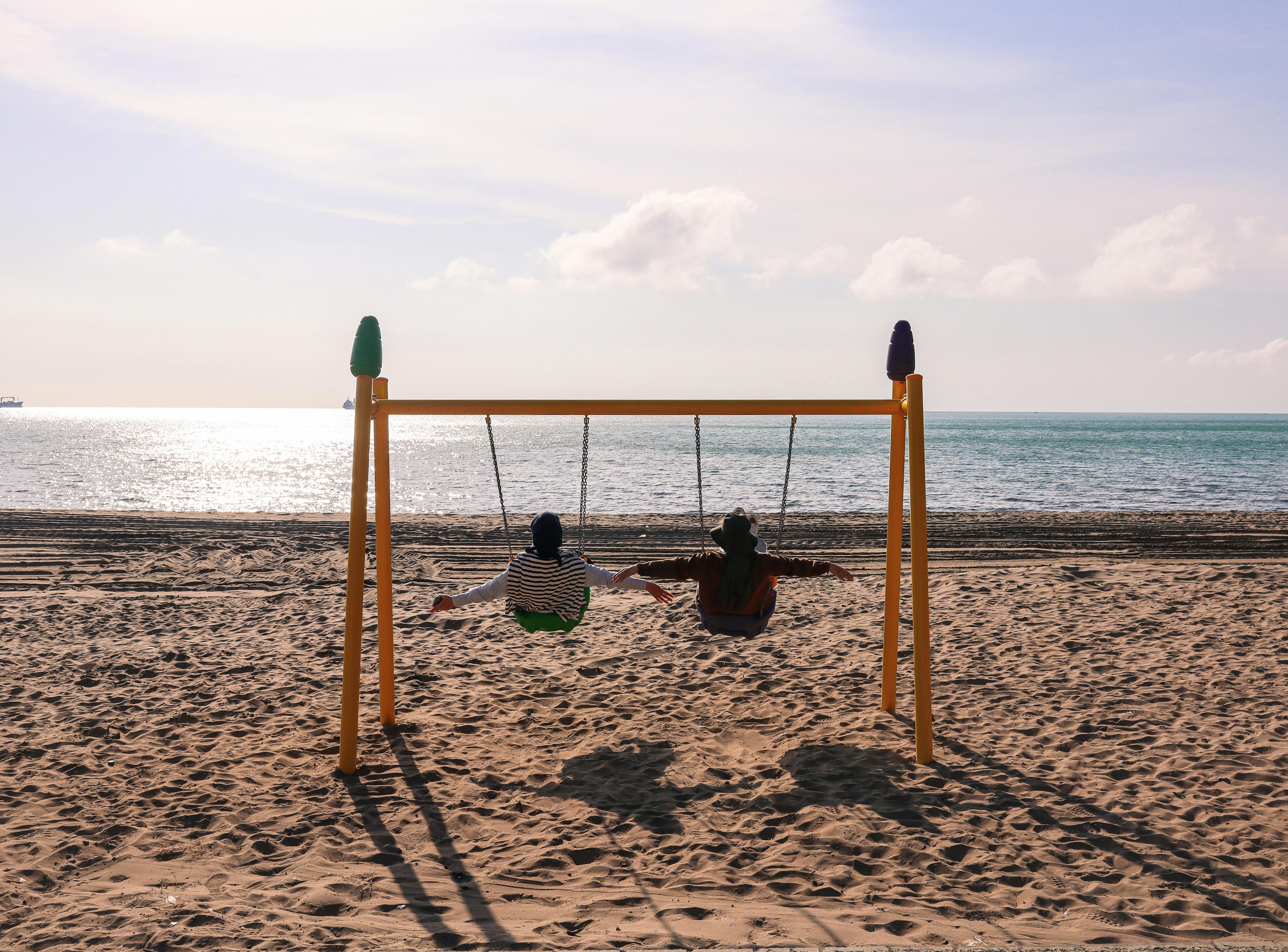 Two Girls Rocking on Swings at a Sunny Beach · Free Stock Photo