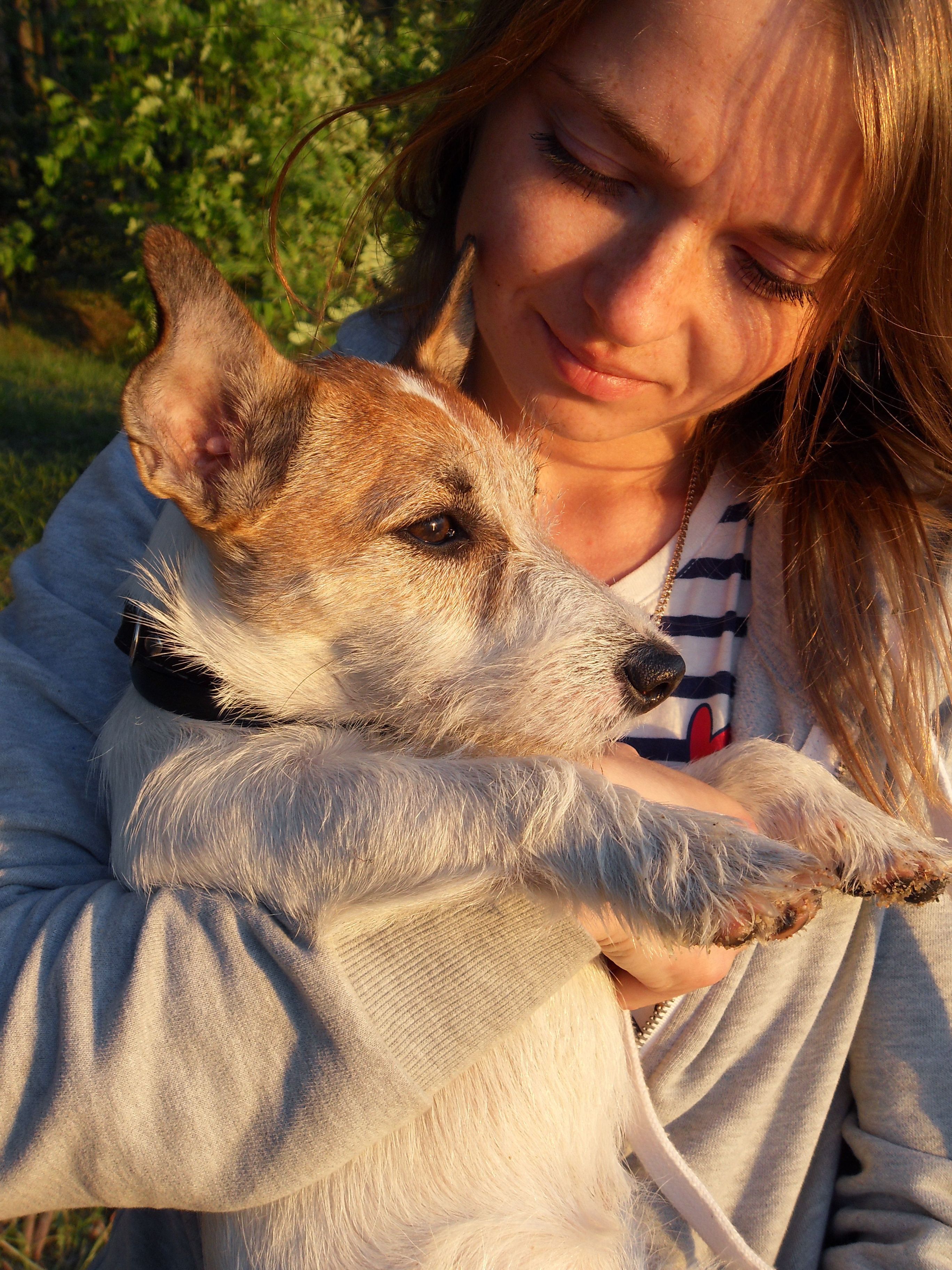 Smiling Woman Carrying Dog Near Tree · Free Stock Photo