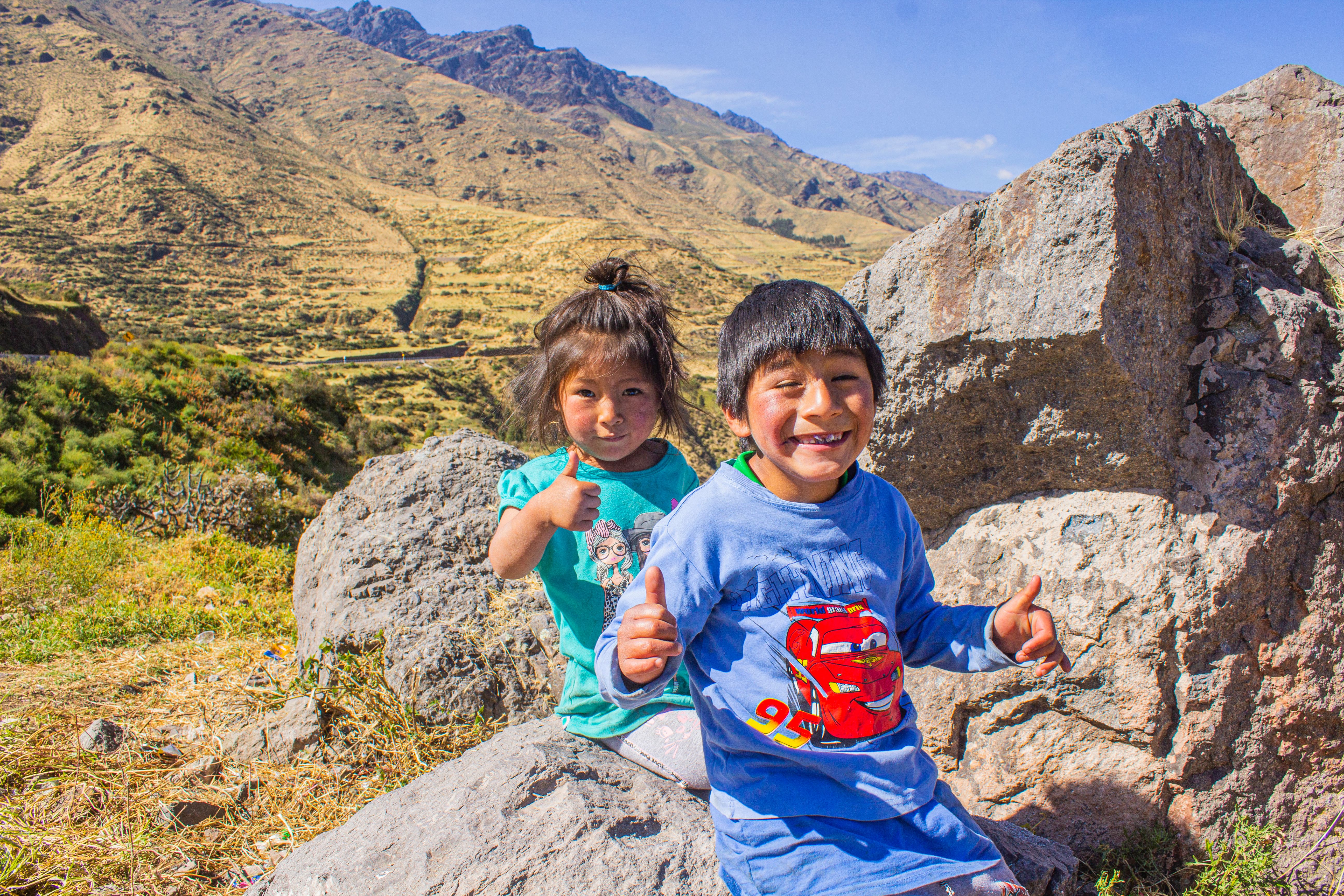 Smiling Children Sitting on Rocks in Mountains Landscape · Free Stock Photo