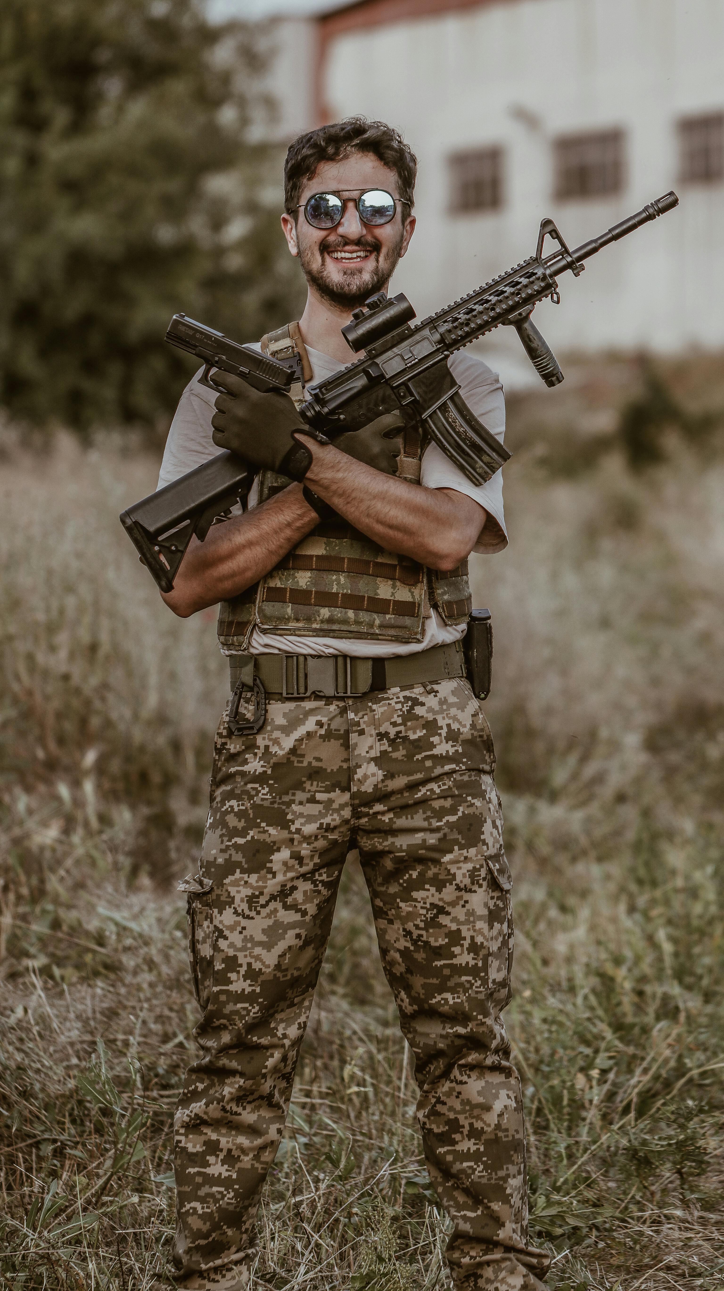 Young Man in Military Uniform Posing with a Handgun and Assault Rifle ...