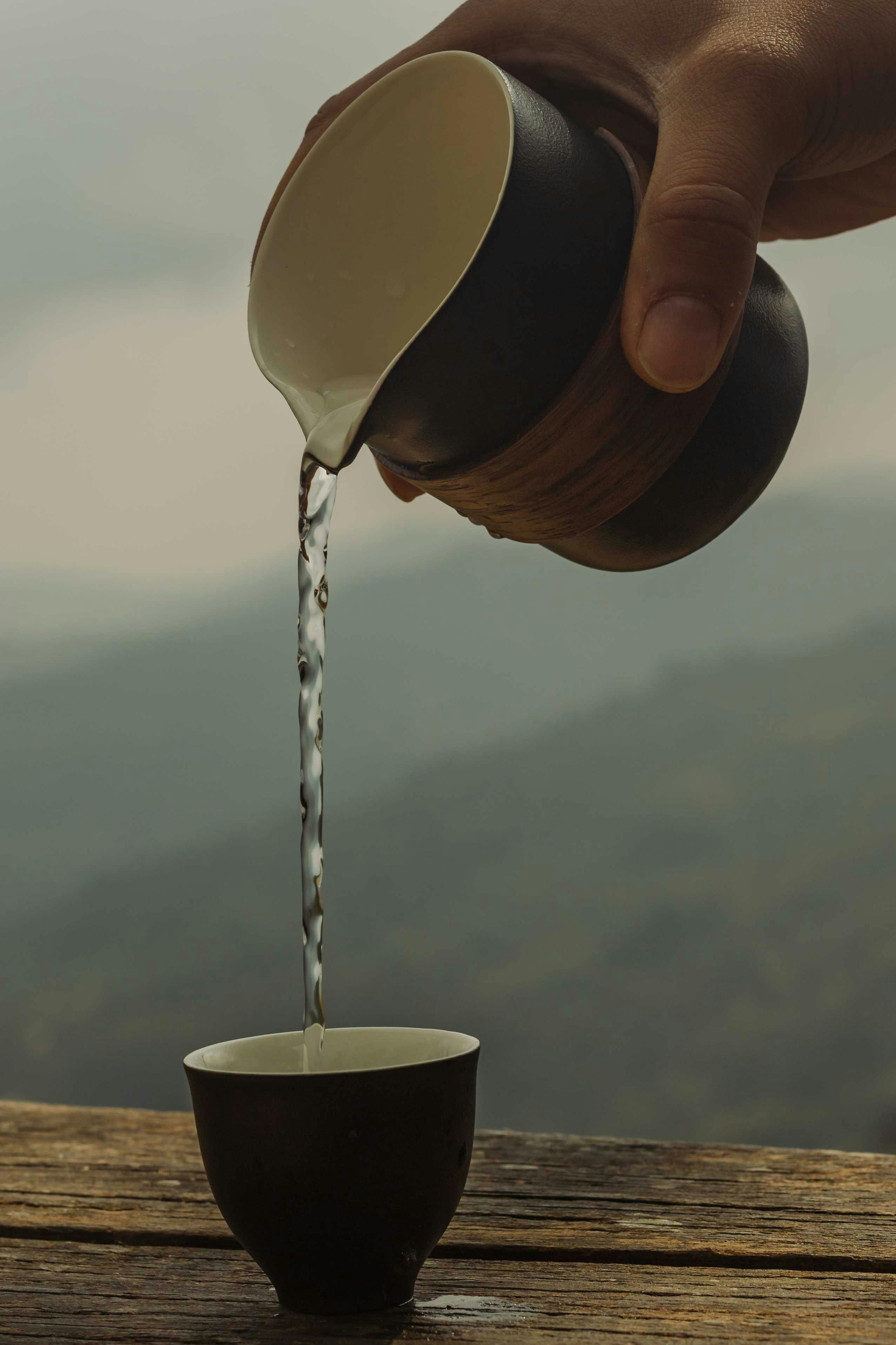 Hand Holding Cup and Pitcher and Pouring Coffee · Free Stock Photo