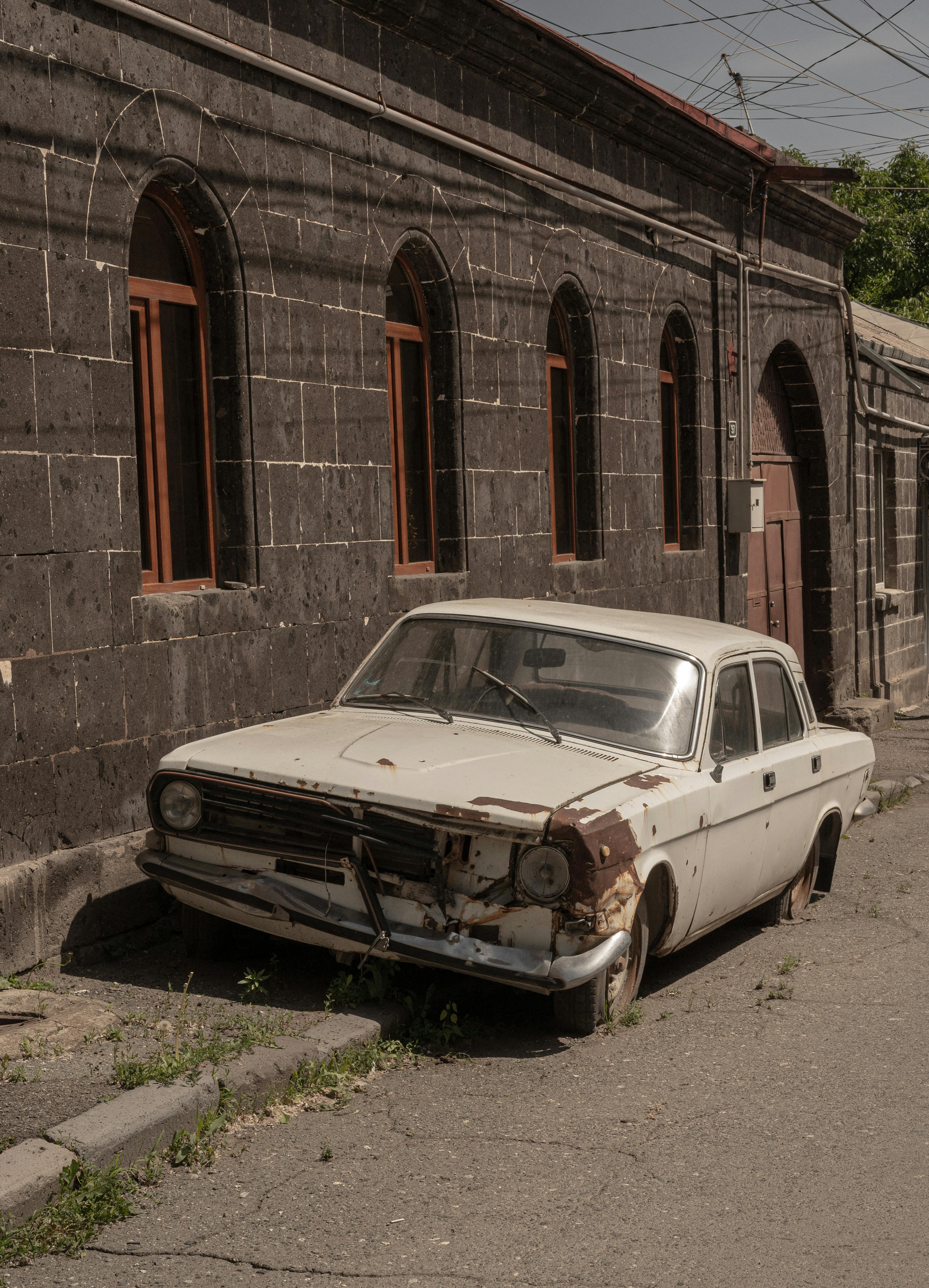 A Broken, Abandoned Car Parked by a Building · Free Stock Photo