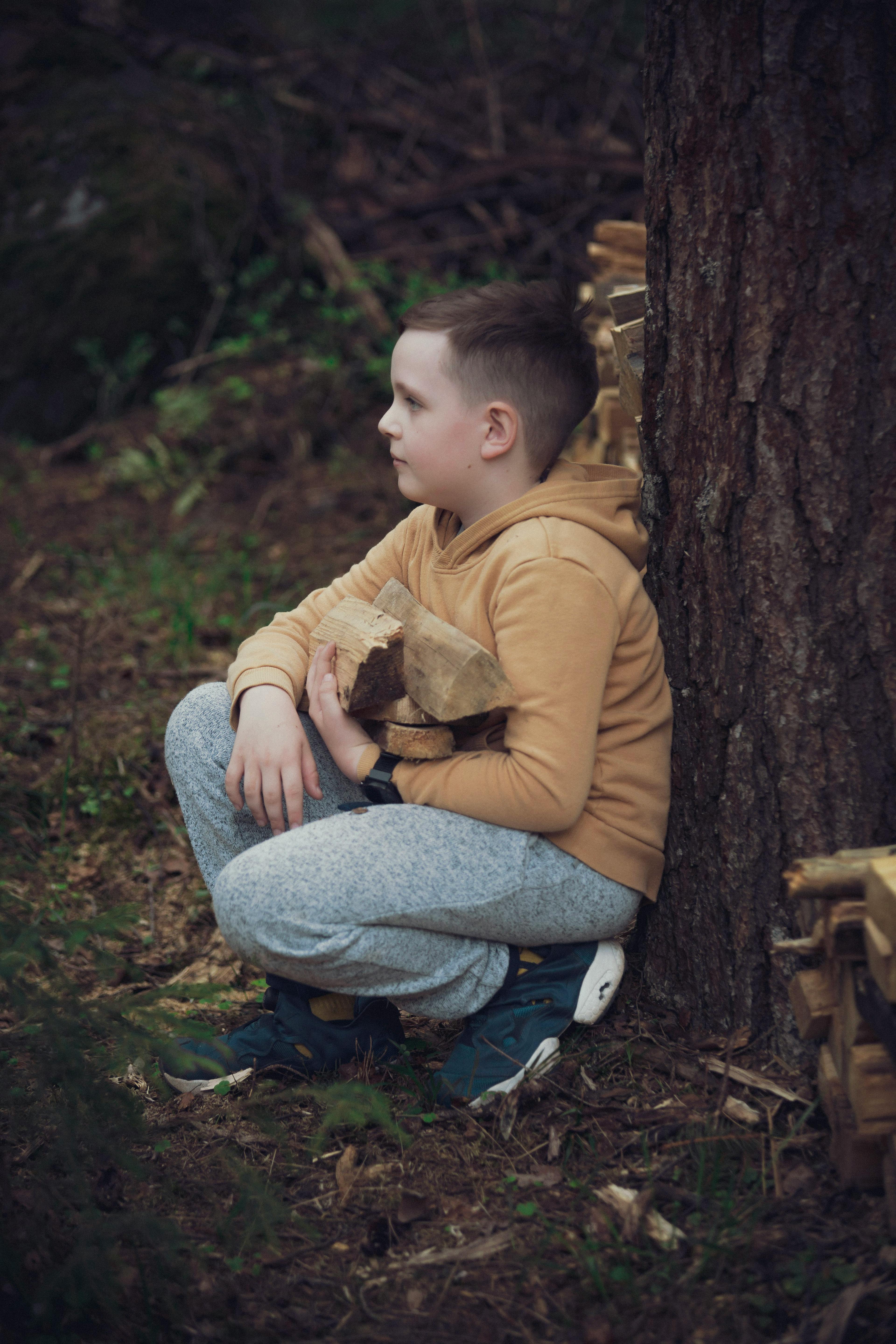 Boy Squatting with Wood in Forest · Free Stock Photo