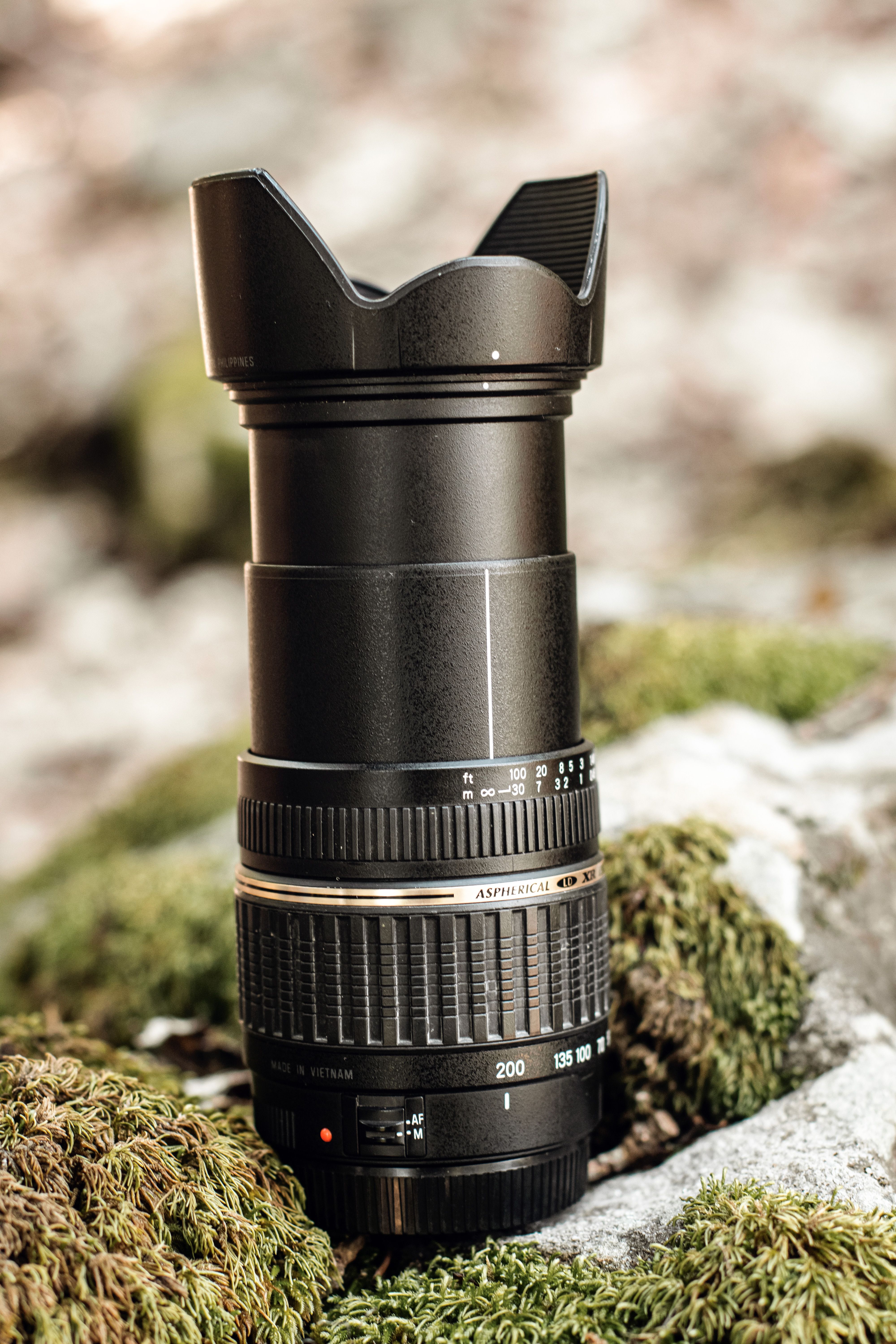 A camera lens sitting on top of a mossy rock · Free Stock Photo