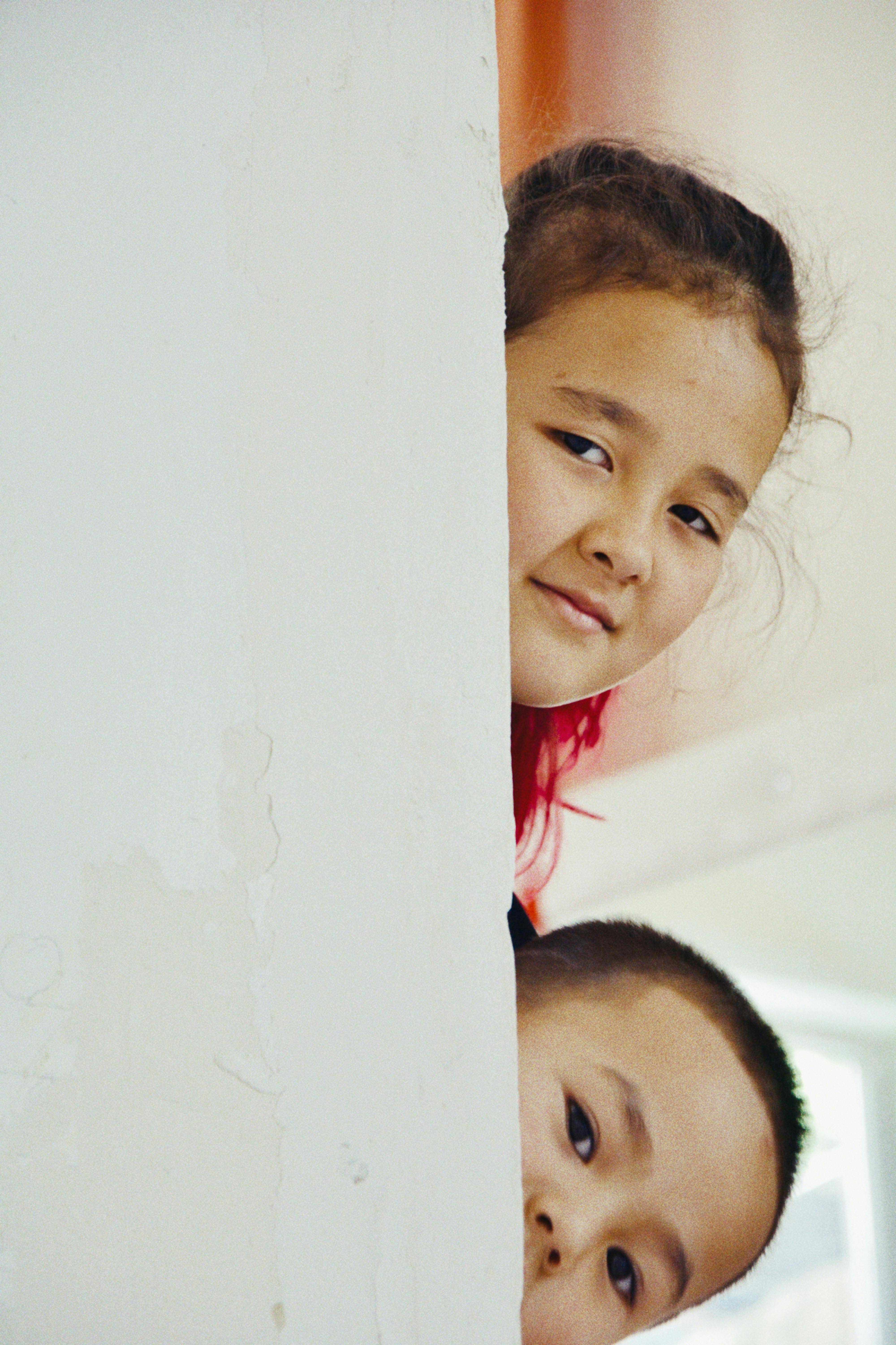 Two children peeking out from behind a wall · Free Stock Photo