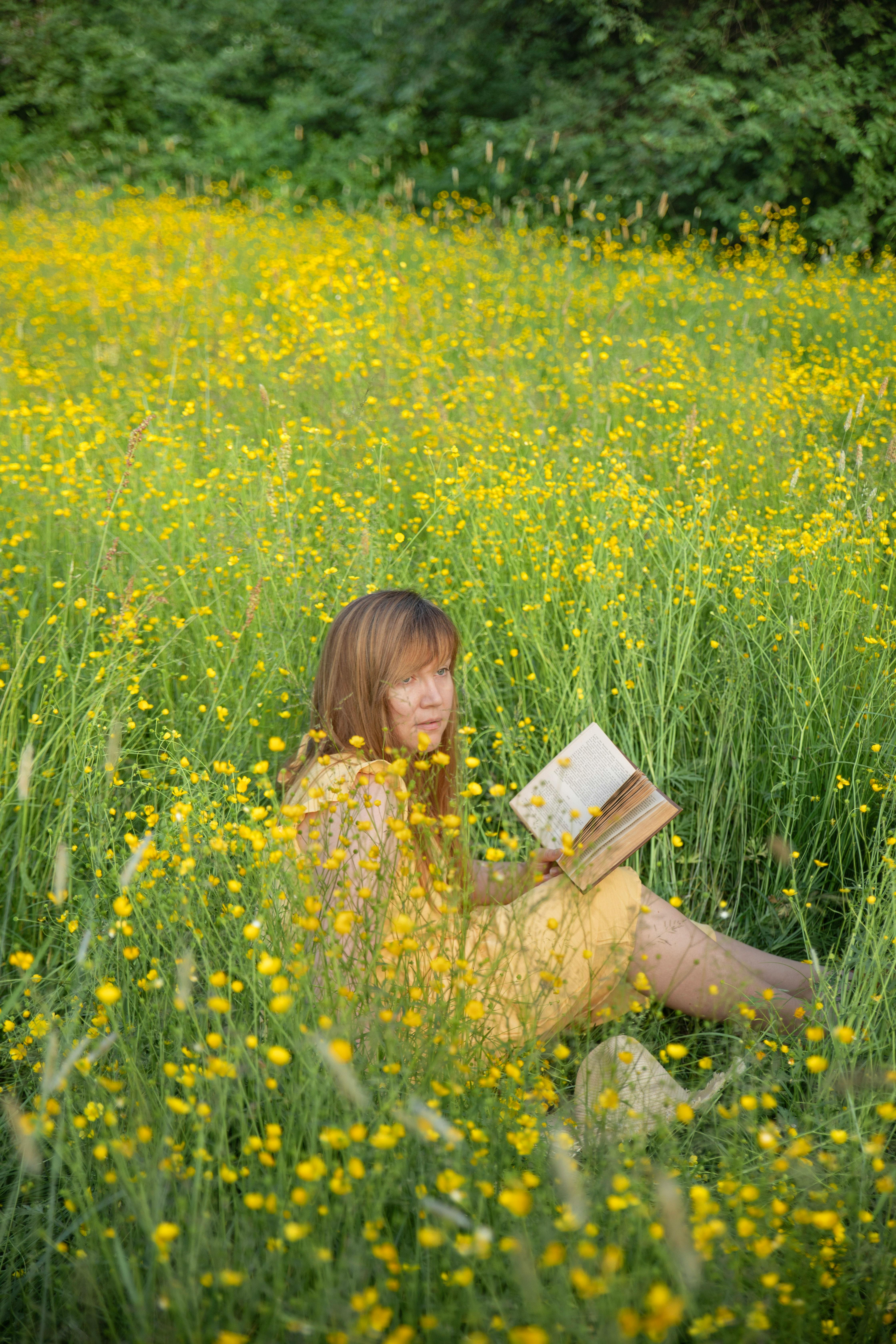 A Woman in a Yellow Dress Reading a Book on a Meadow with Yellow ...