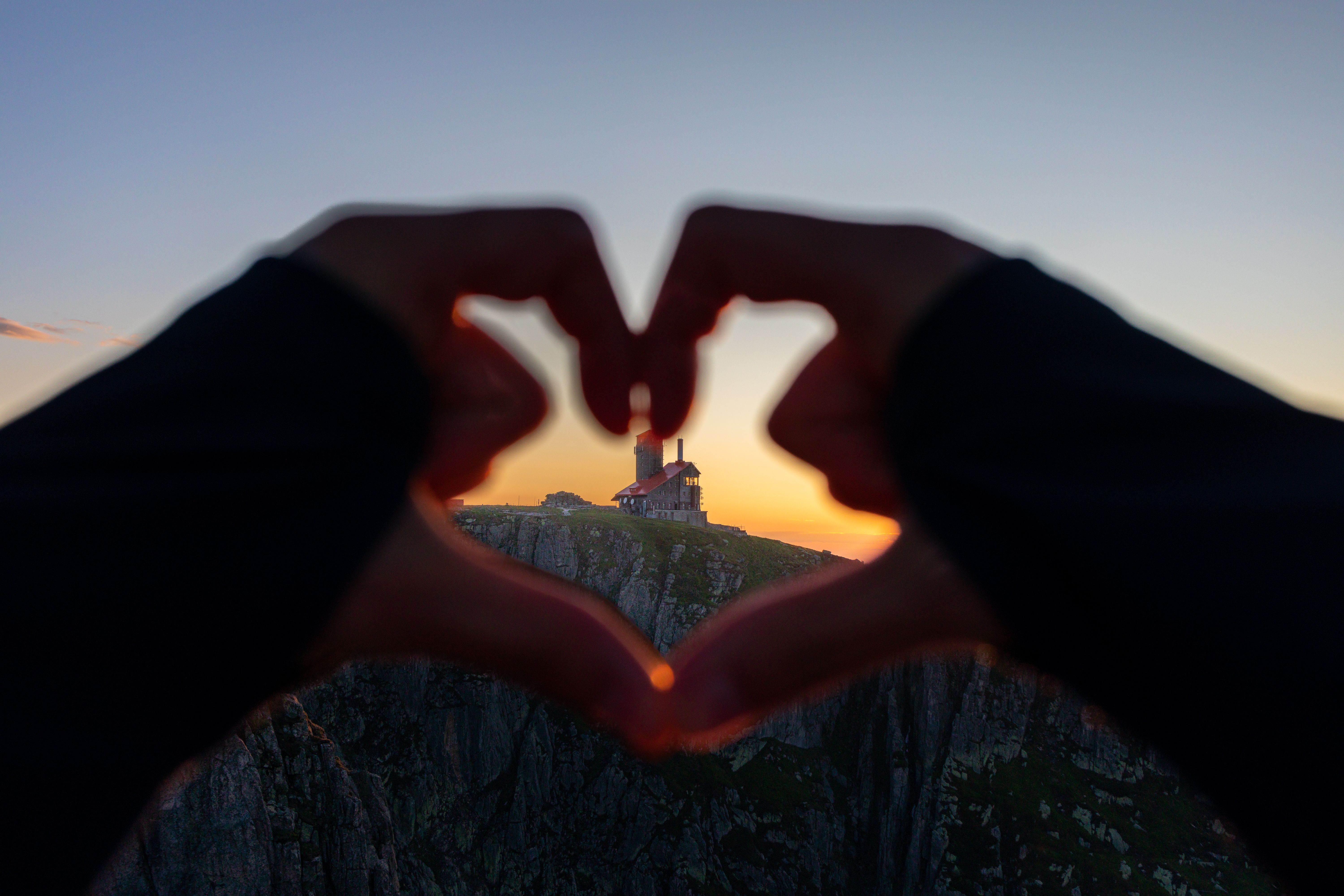 Cliff and Building behind Hands in Heart Shape at Sunset · Free Stock Photo