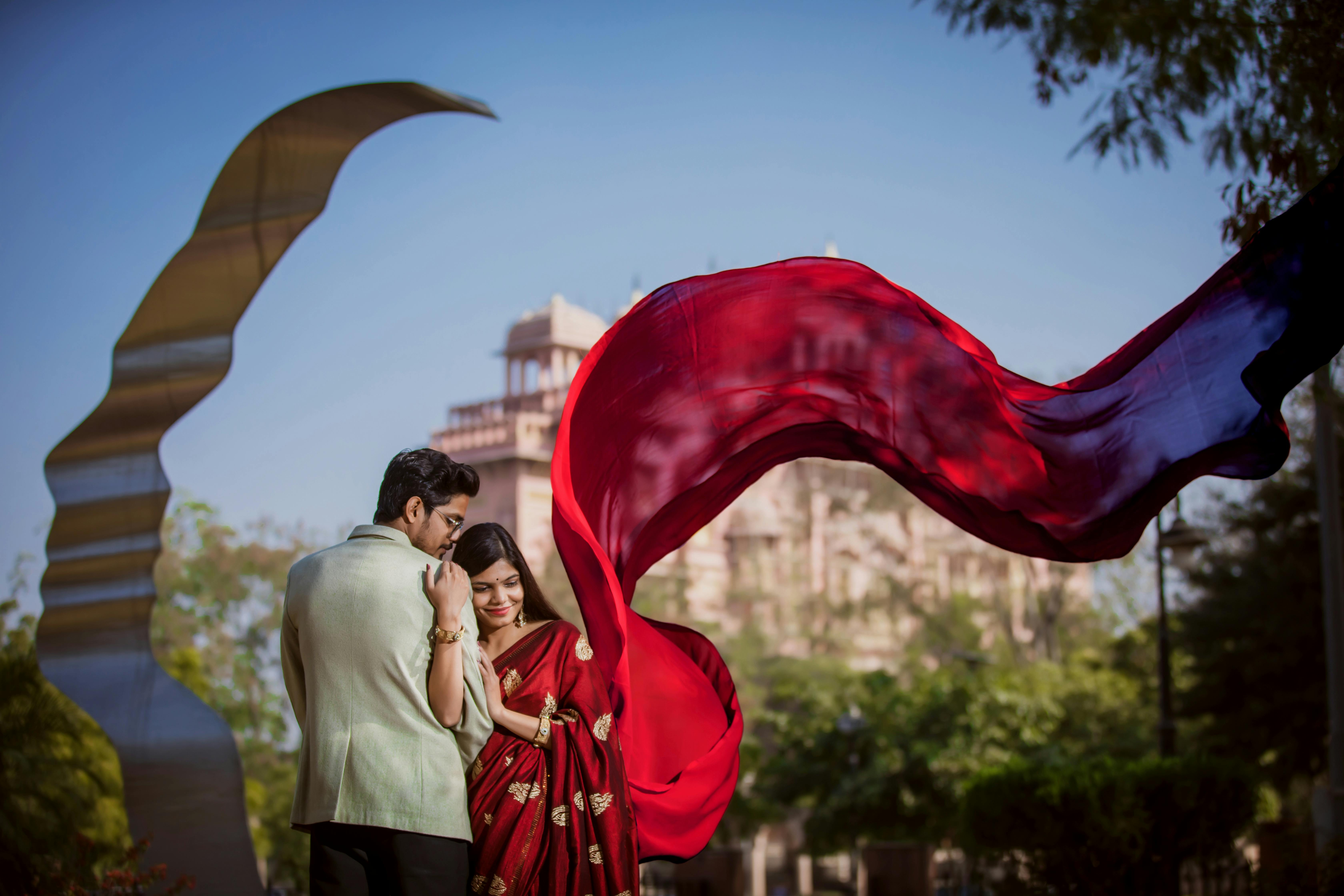 Woman in Red Dress Billowing in Wind Embracing Man · Free Stock Photo