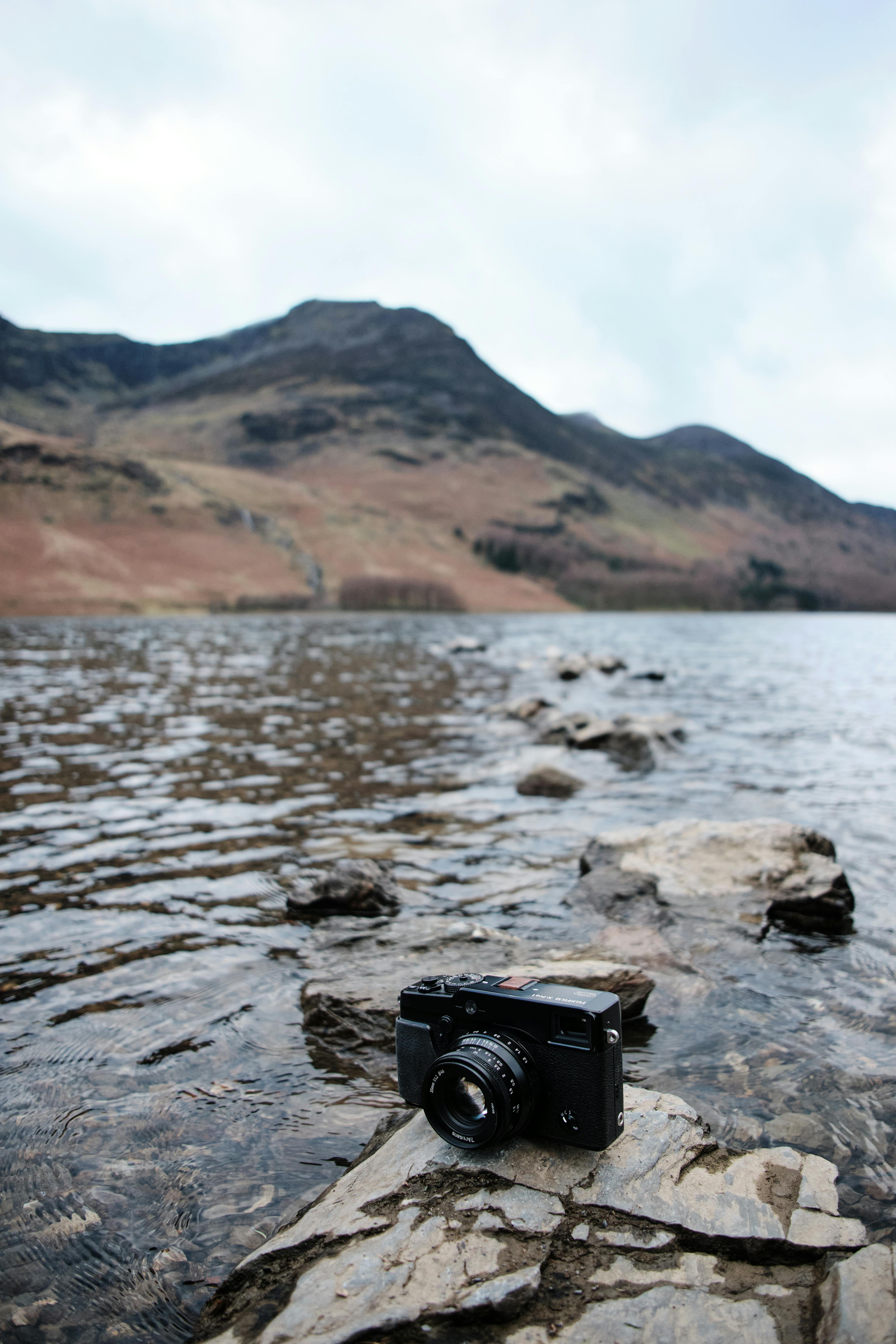 Camera on Stones on Shore with Hill behind · Free Stock Photo