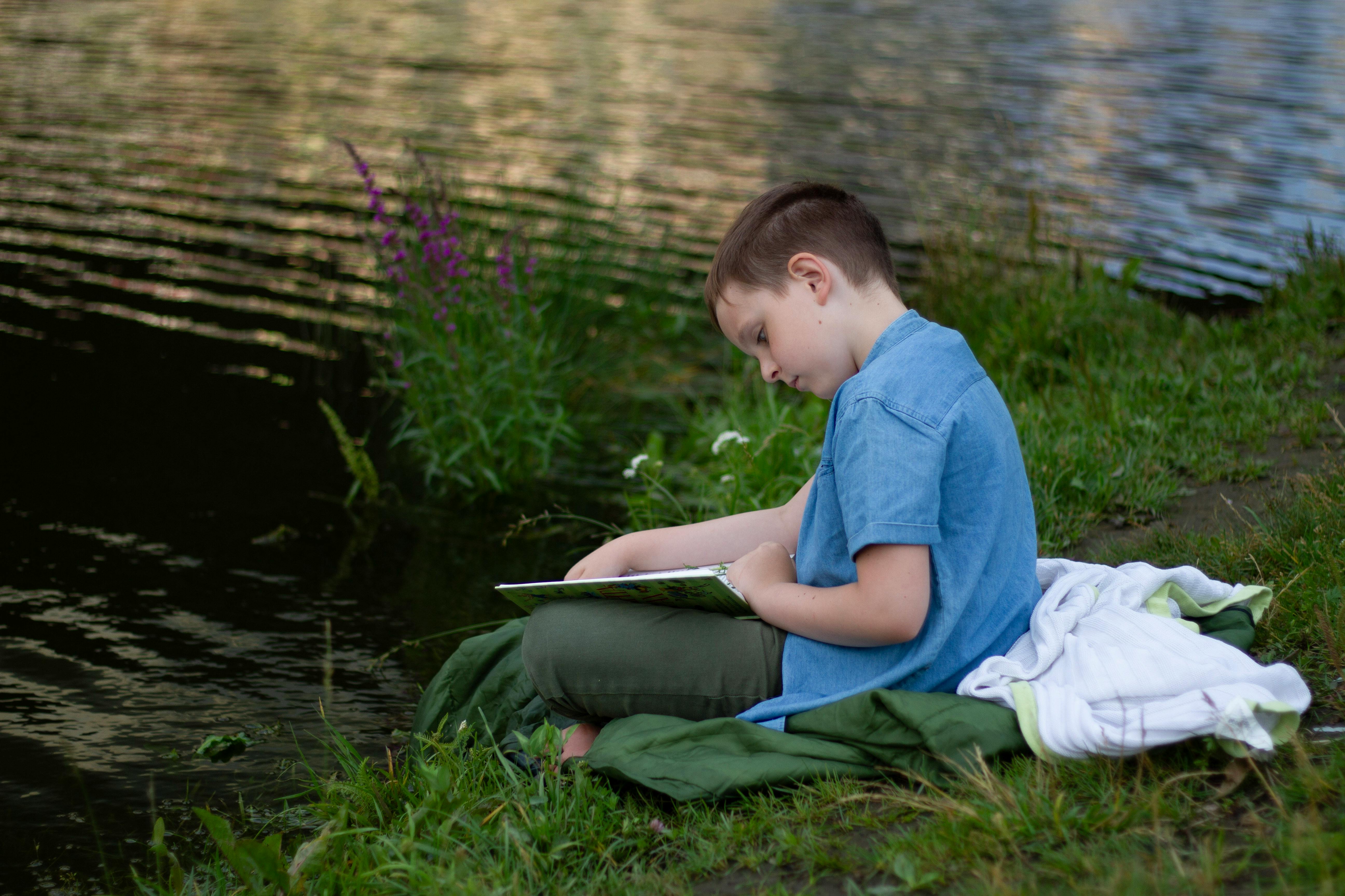 Child Sitting by River and Reading · Free Stock Photo