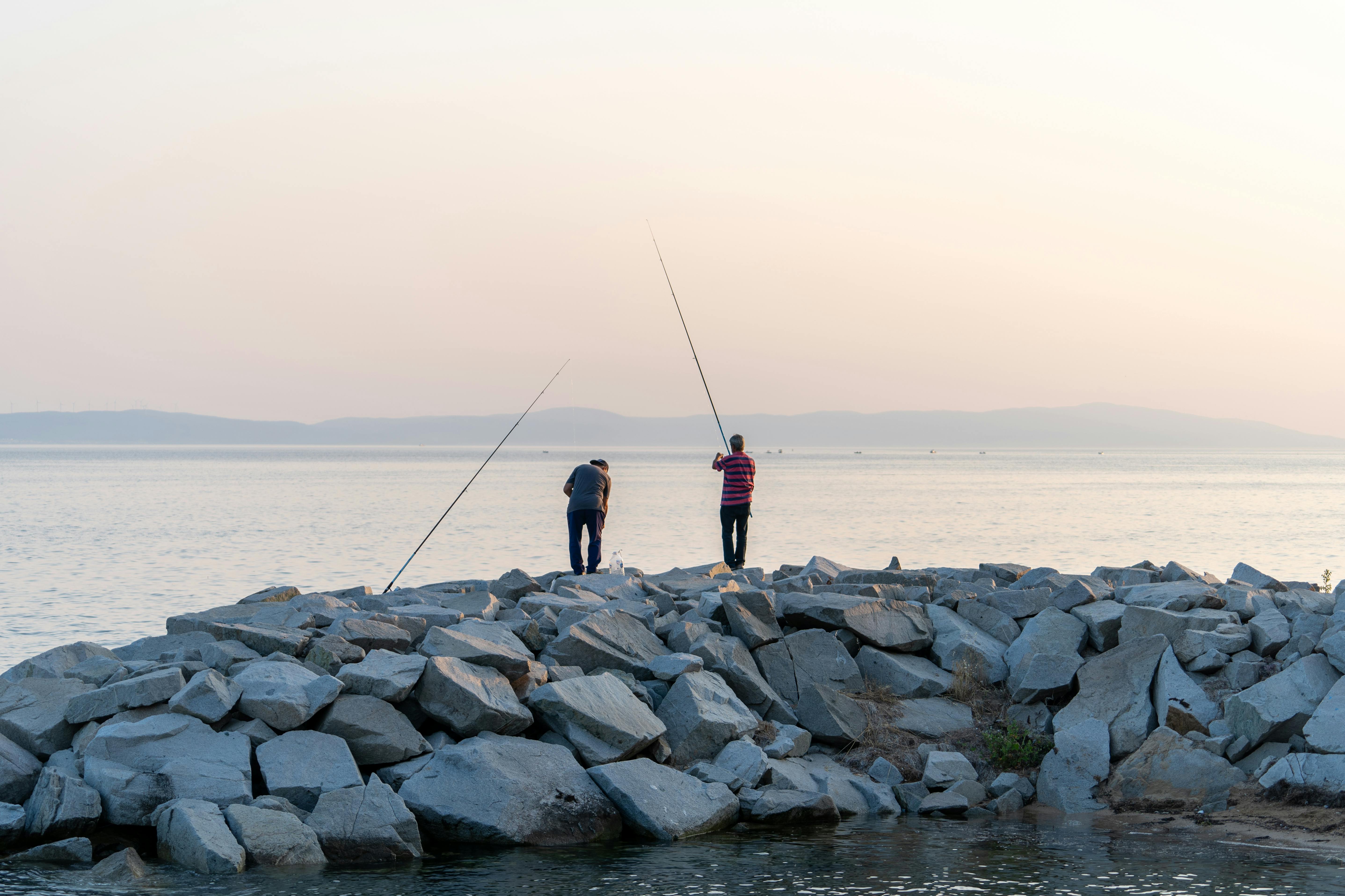 Two people fishing on rocks near the water · Free Stock Photo