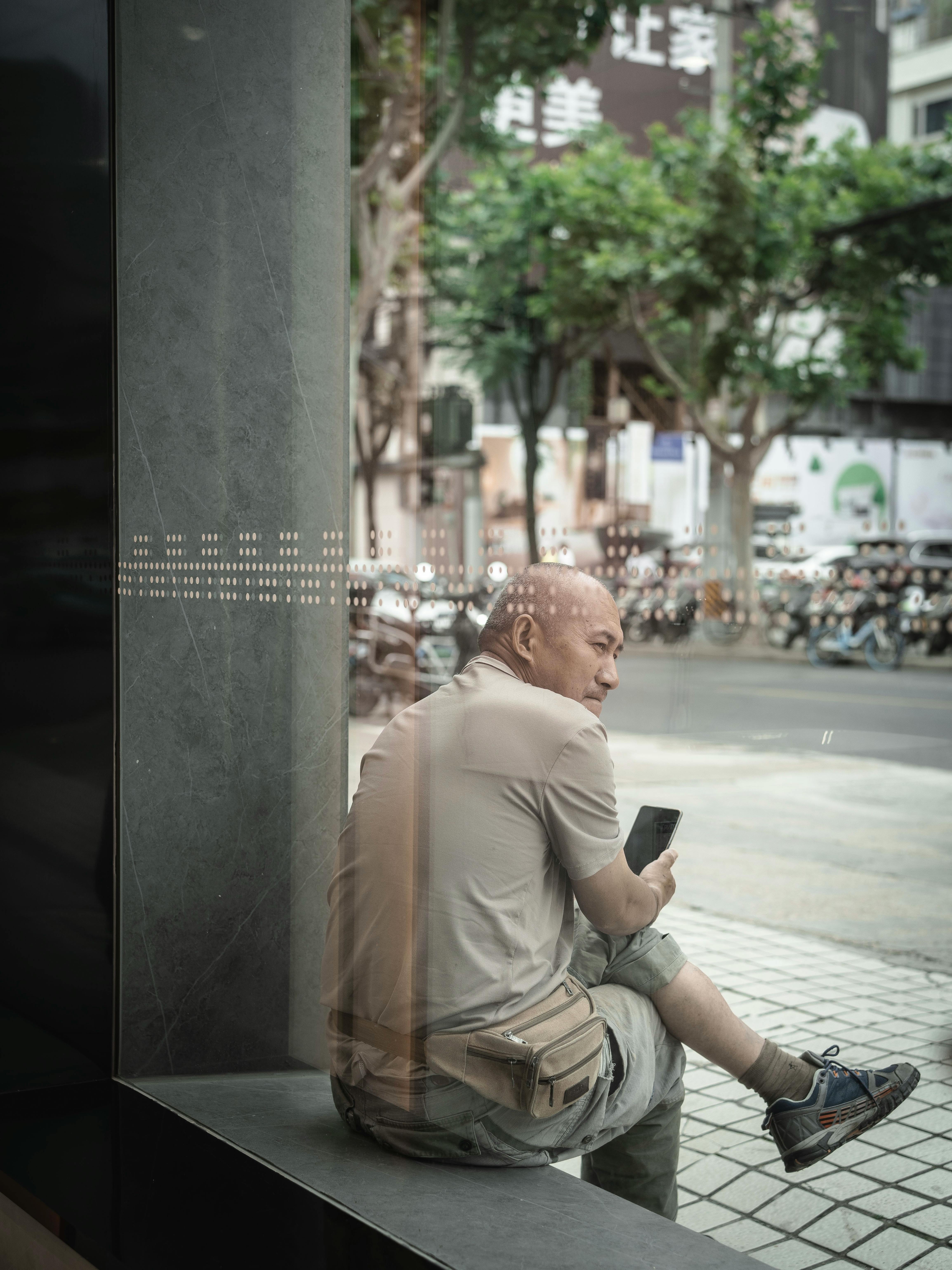 Man Sitting on a Window Parapet with a Smart Phone and Watching the ...
