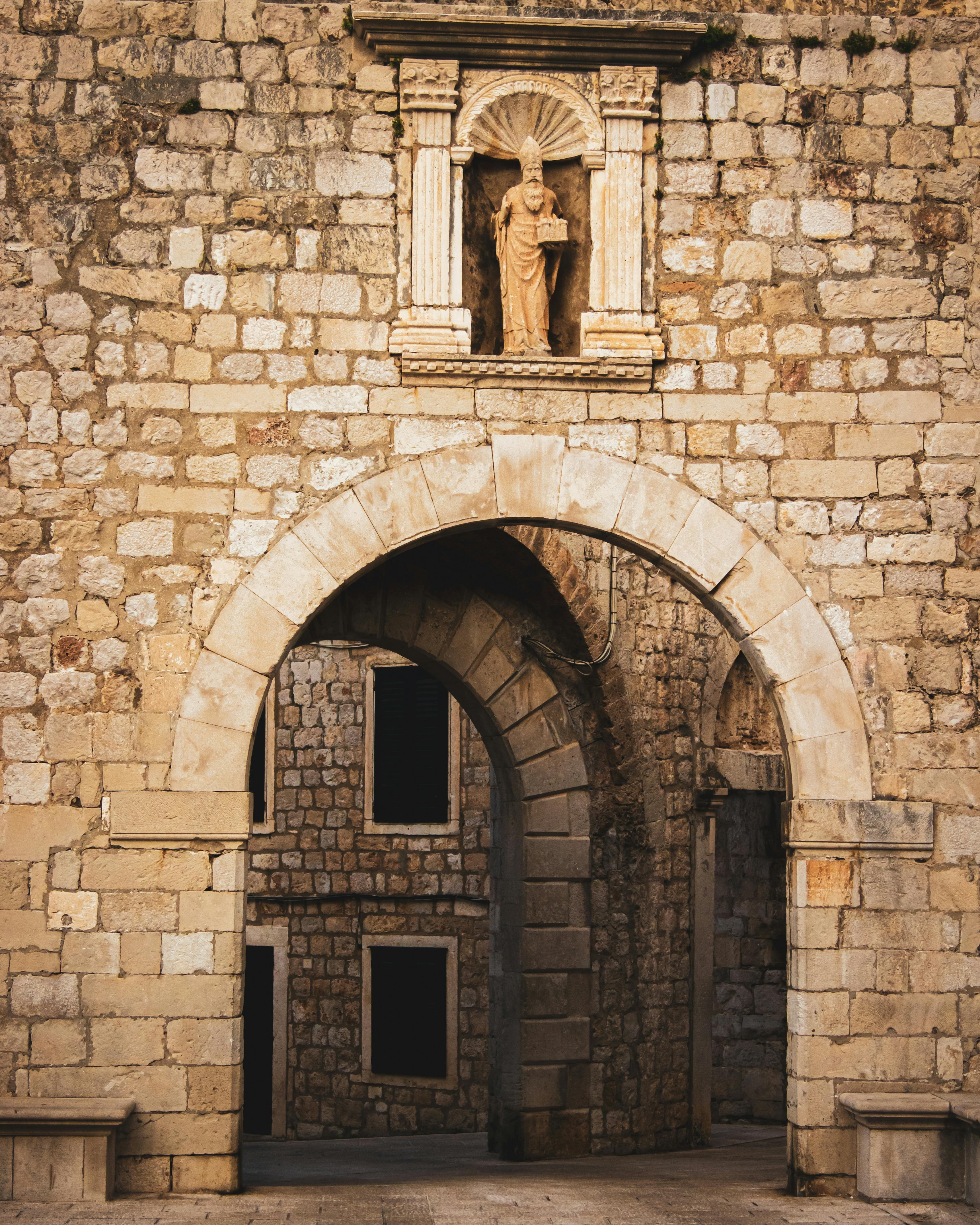 A stone archway with a statue in it · Free Stock Photo