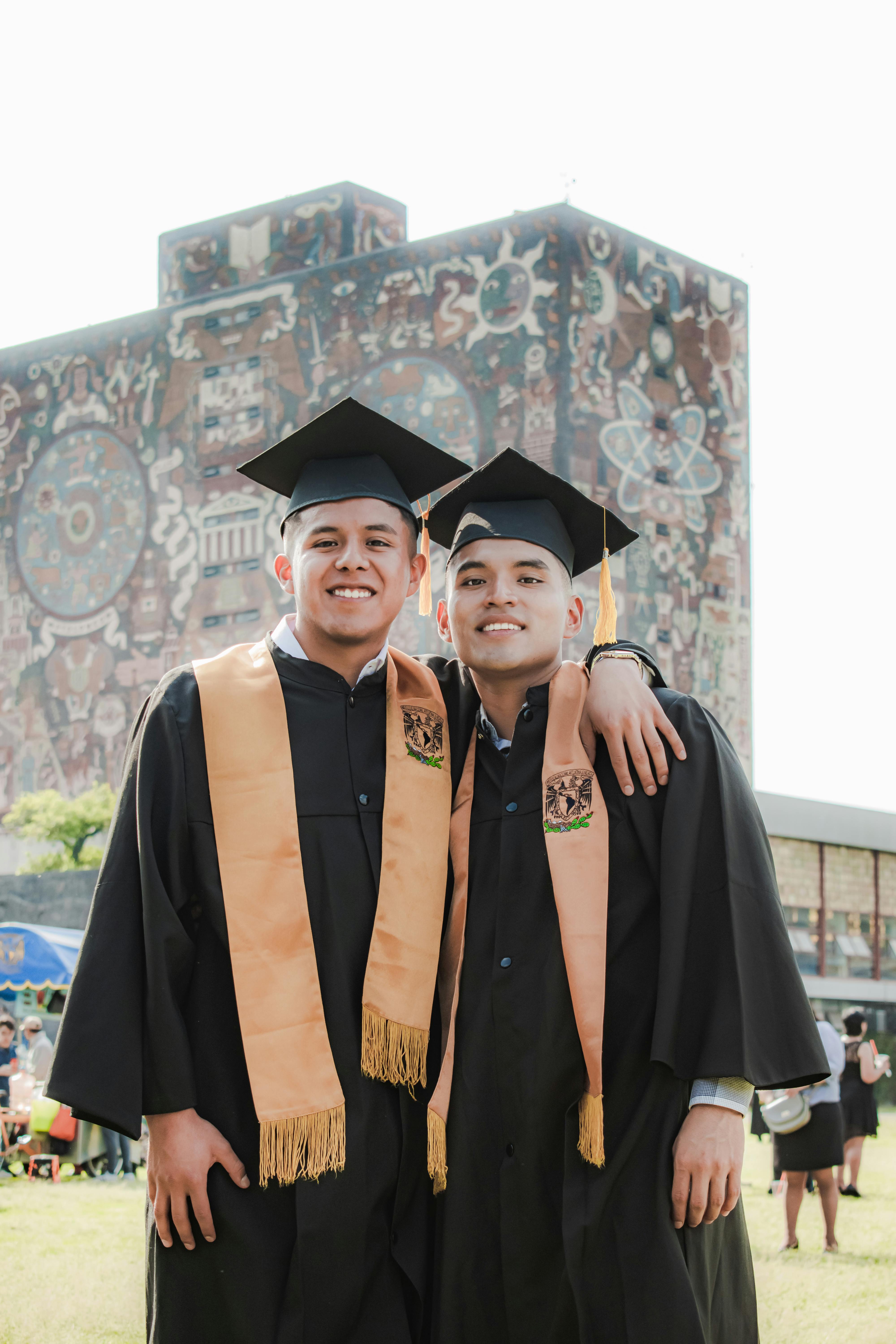 Two Alumni Men in Graduation Gowns and Caps Posing at a University ...