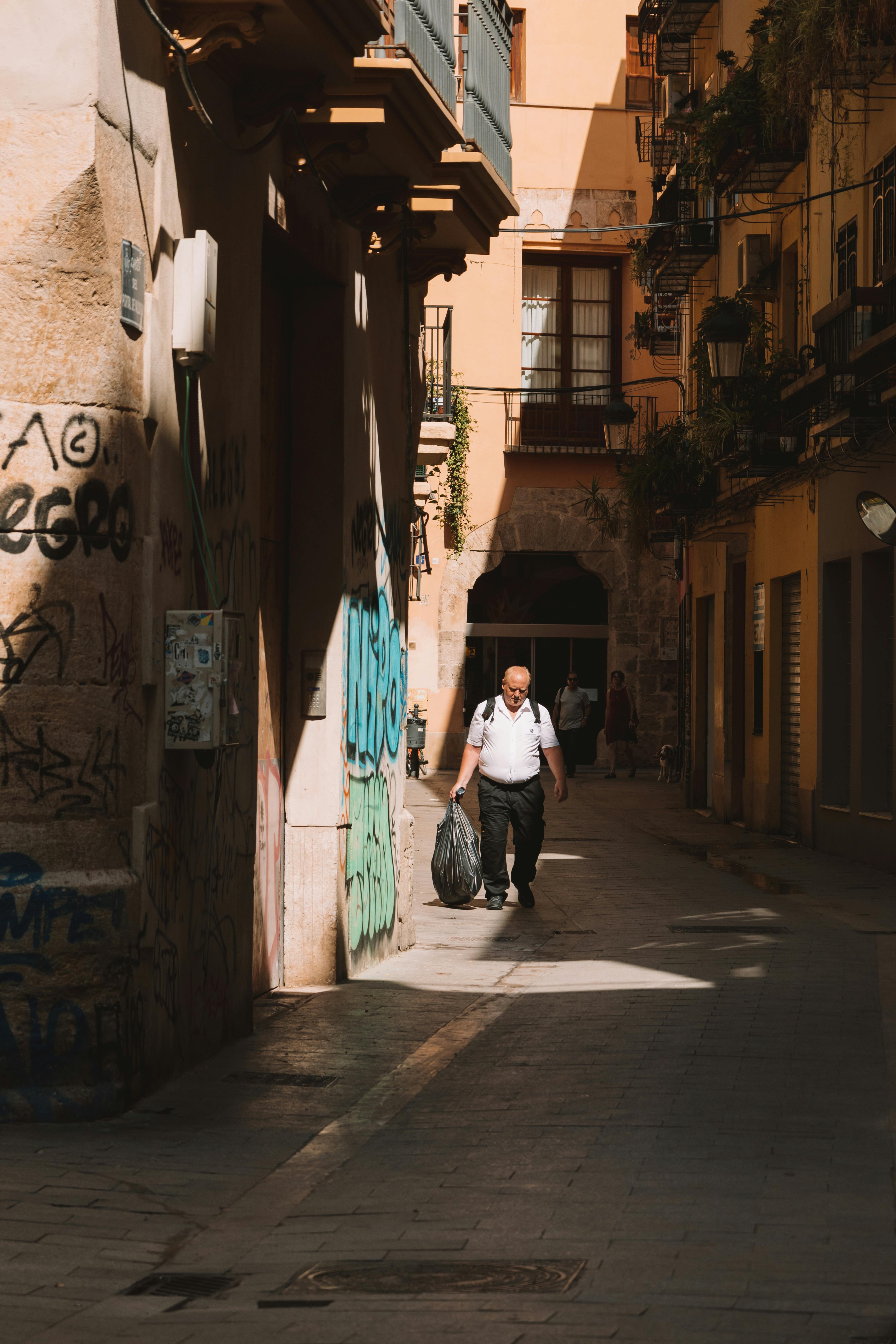 Man with a Garbage Bag Walking in the City Alley · Free Stock Photo