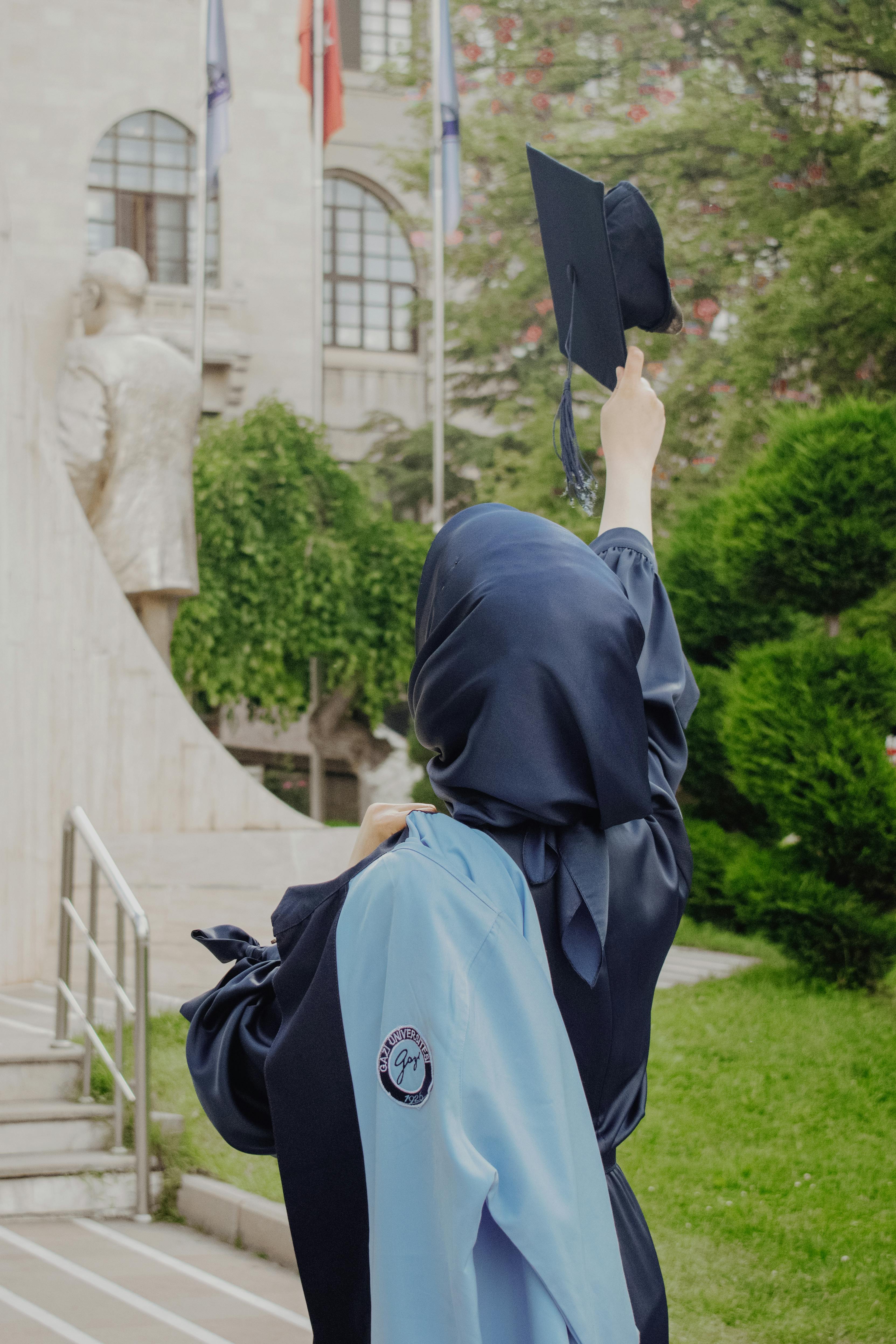 Graduate in Hijab and Gown Holding Academic Hat near Walls of Anitkabir ...
