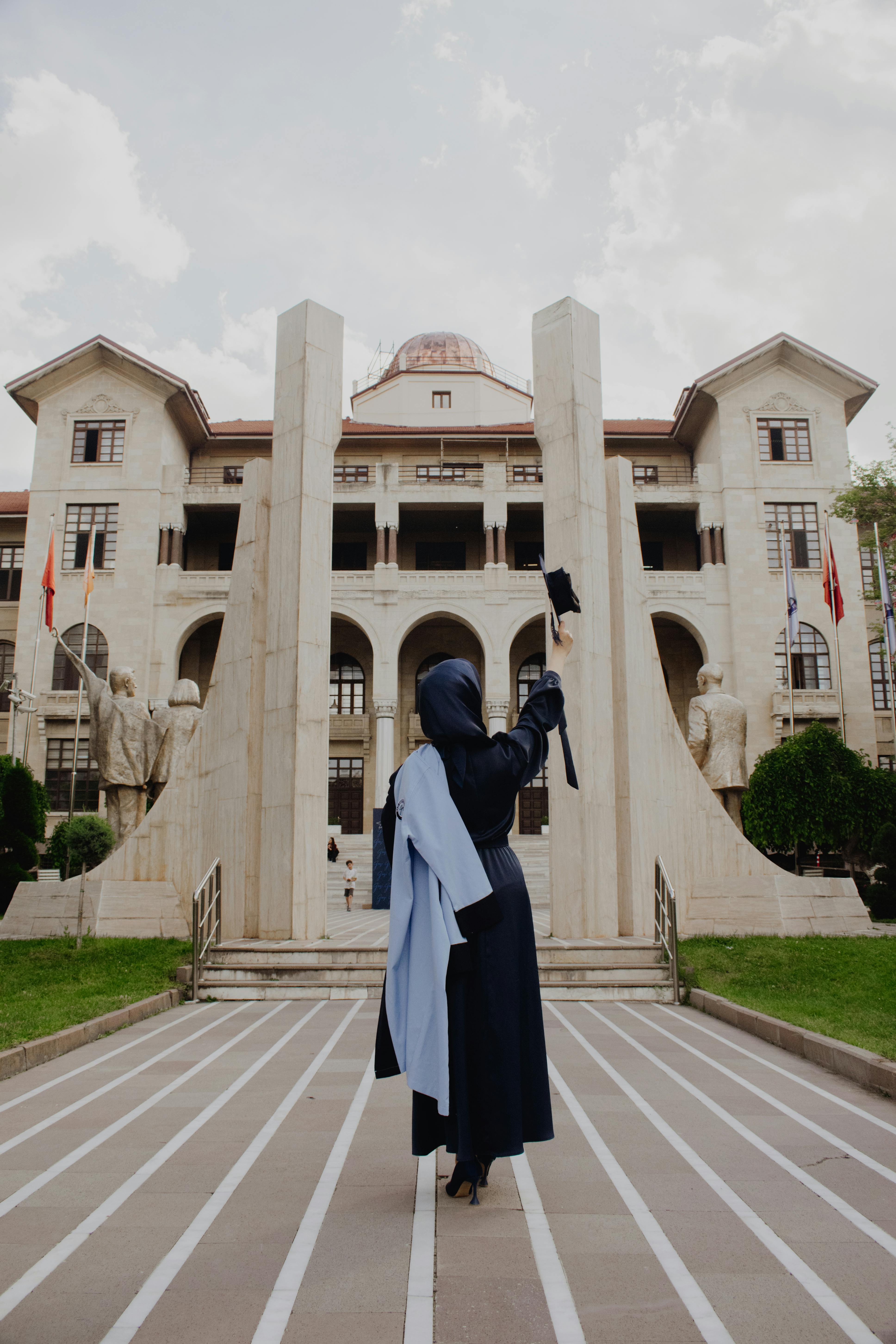 Graduate in Hijab and Gown Holding Academic Hat near Walls of Anitkabir ...