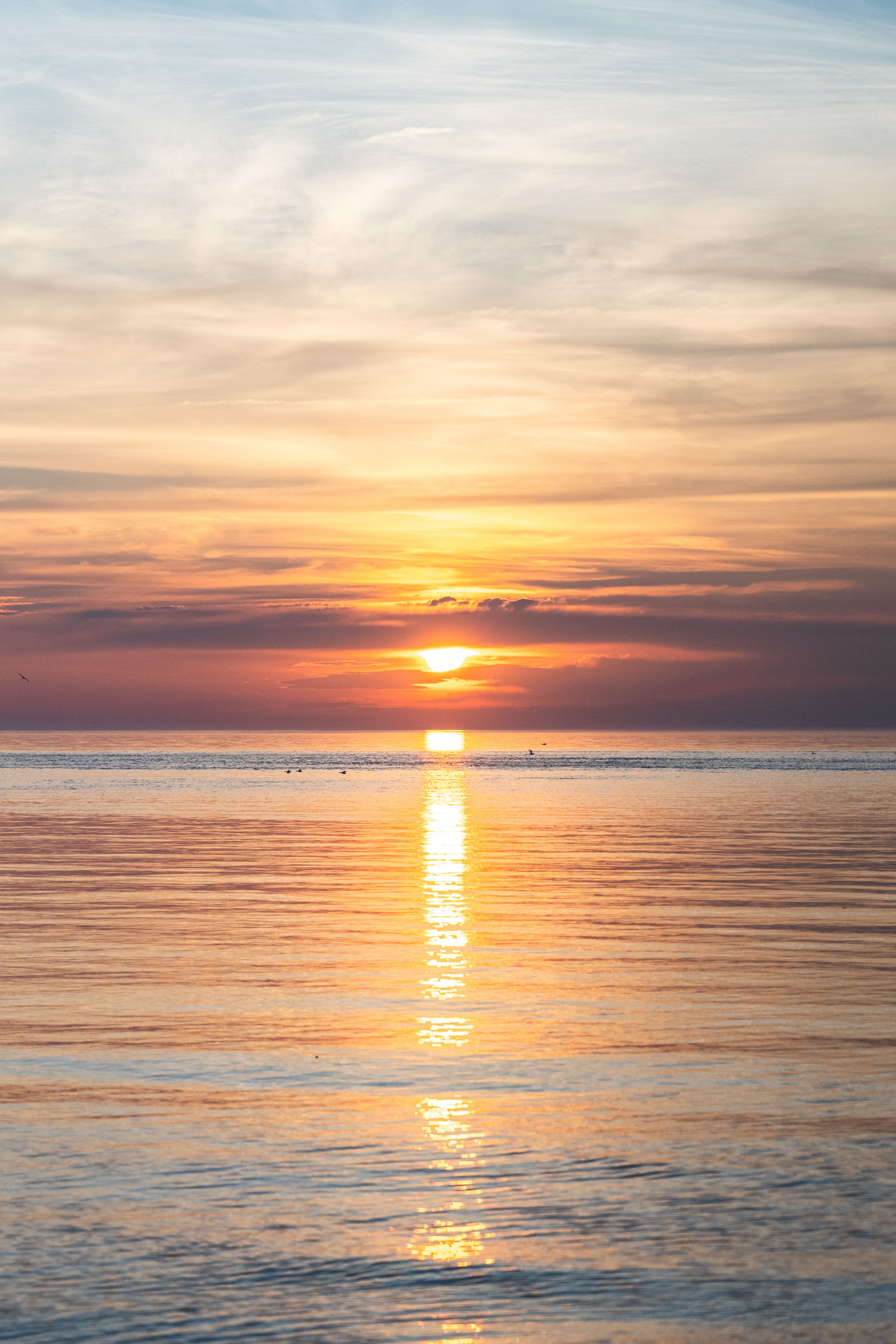 A sunset over the ocean with a boat in the water · Free Stock Photo