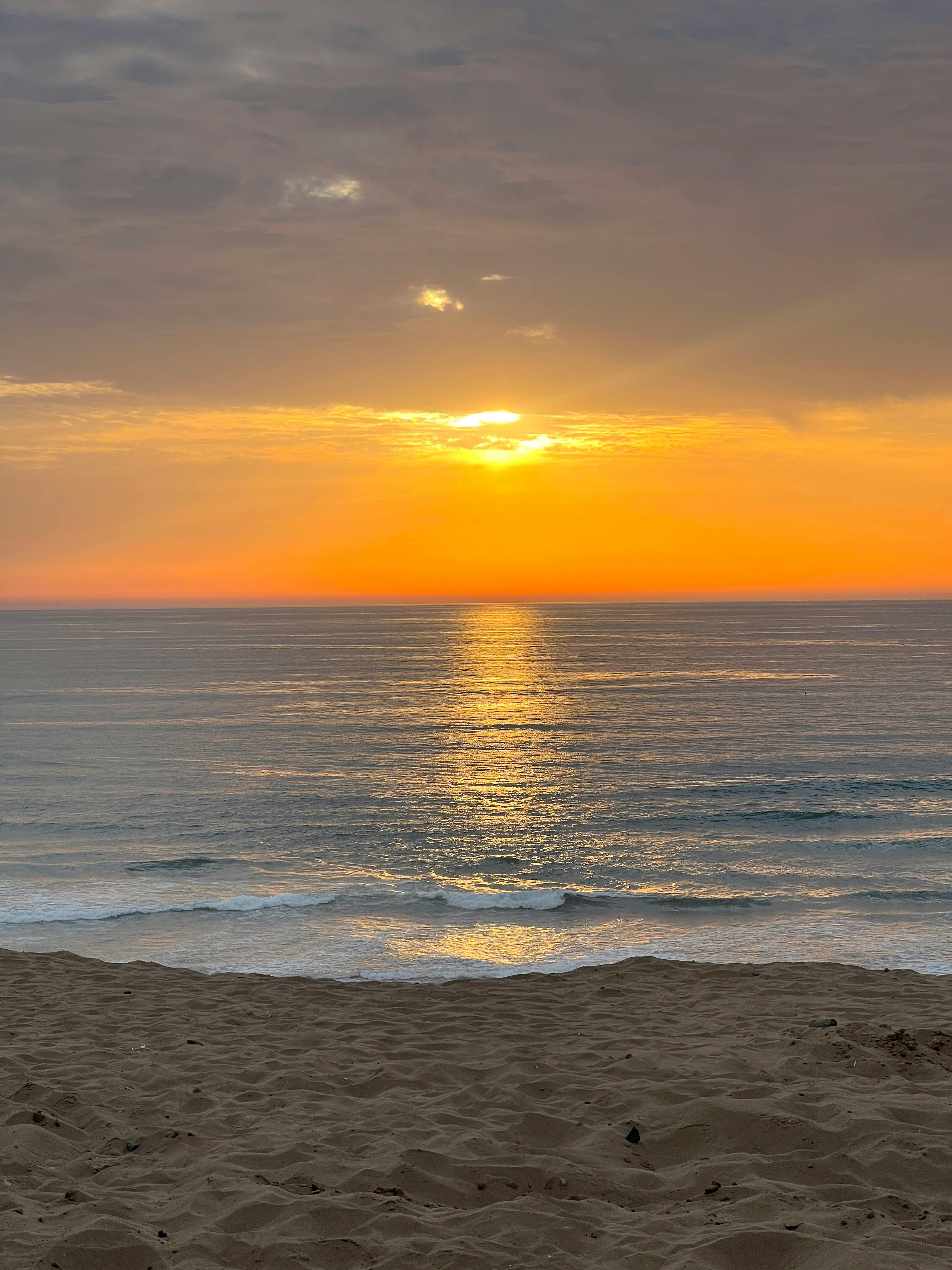 A sunset over the ocean with a person on the beach · Free Stock Photo
