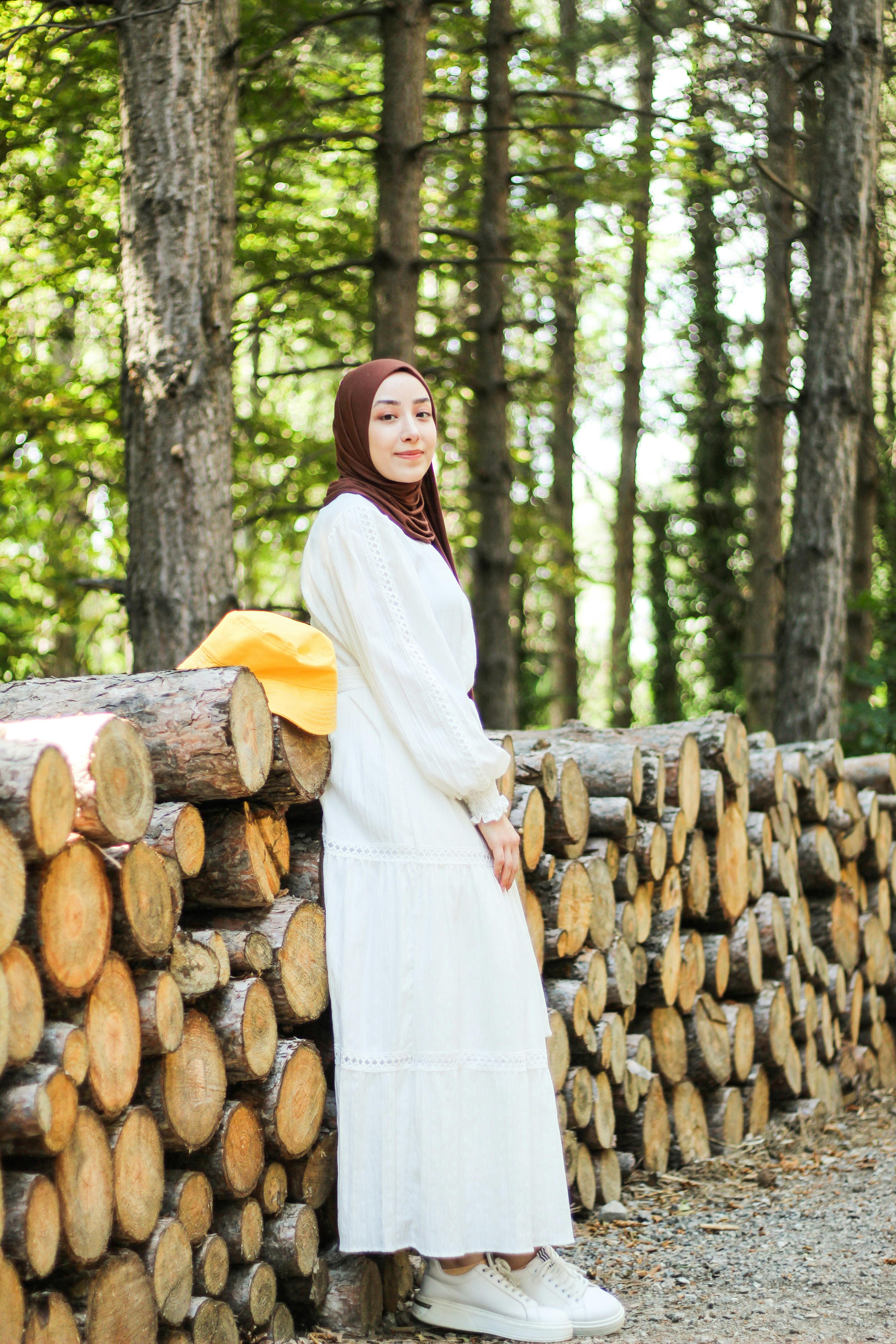 Young Woman in White Dress and Brown Hijab Standing by a Timber Stack ...