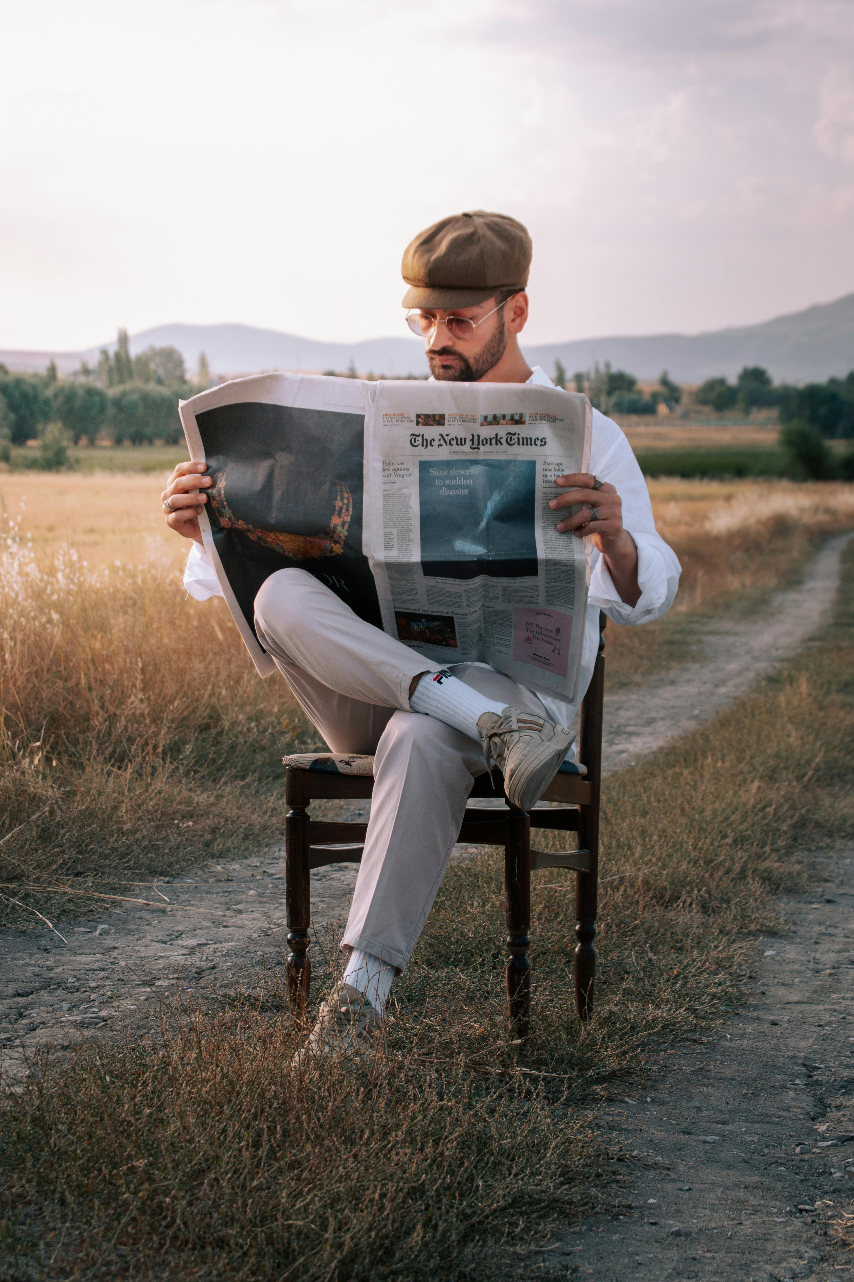Man Sitting in Chair with Newspaper on Country Road · Free Stock Photo