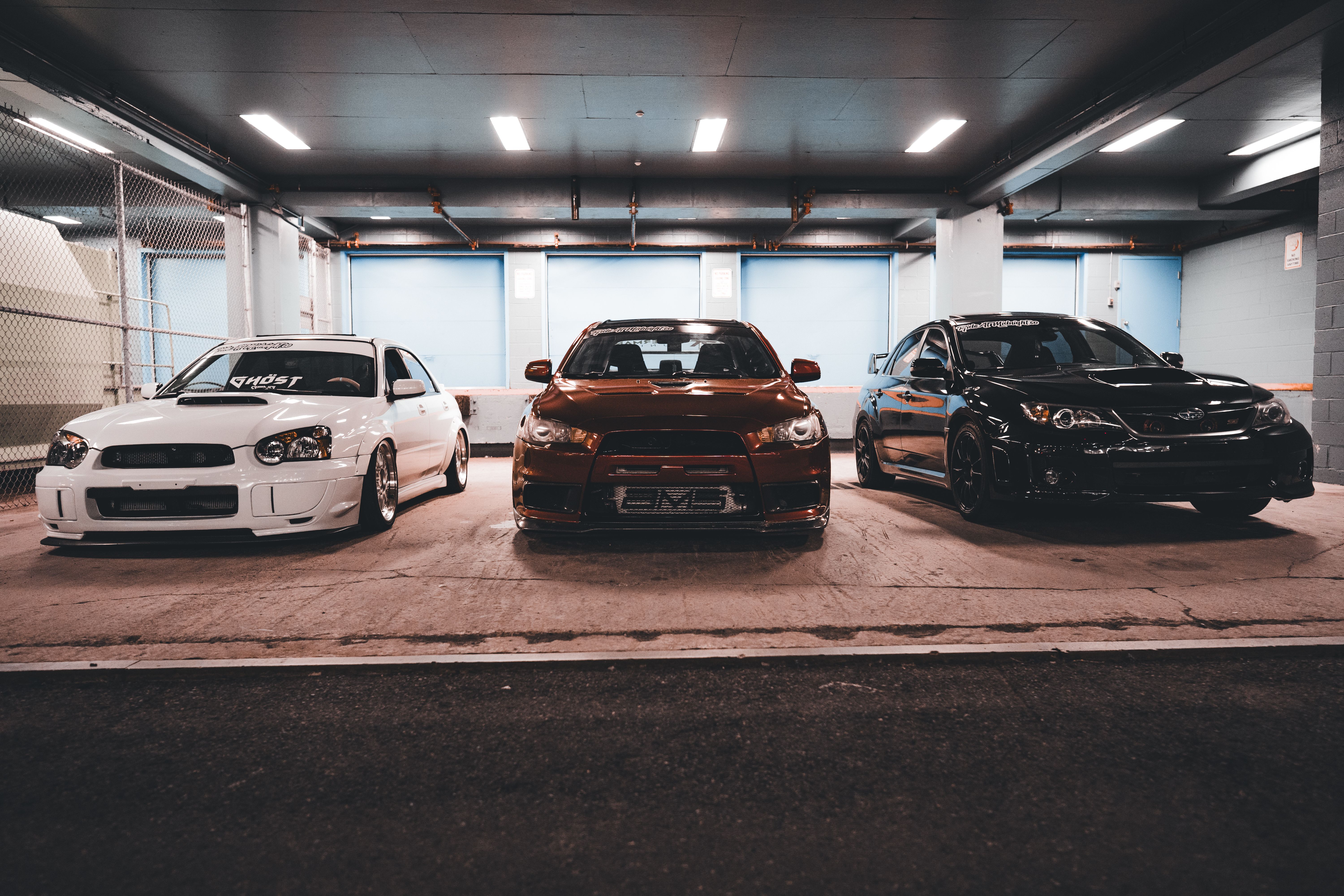 Three cars parked in a garage with a white wall · Free Stock Photo