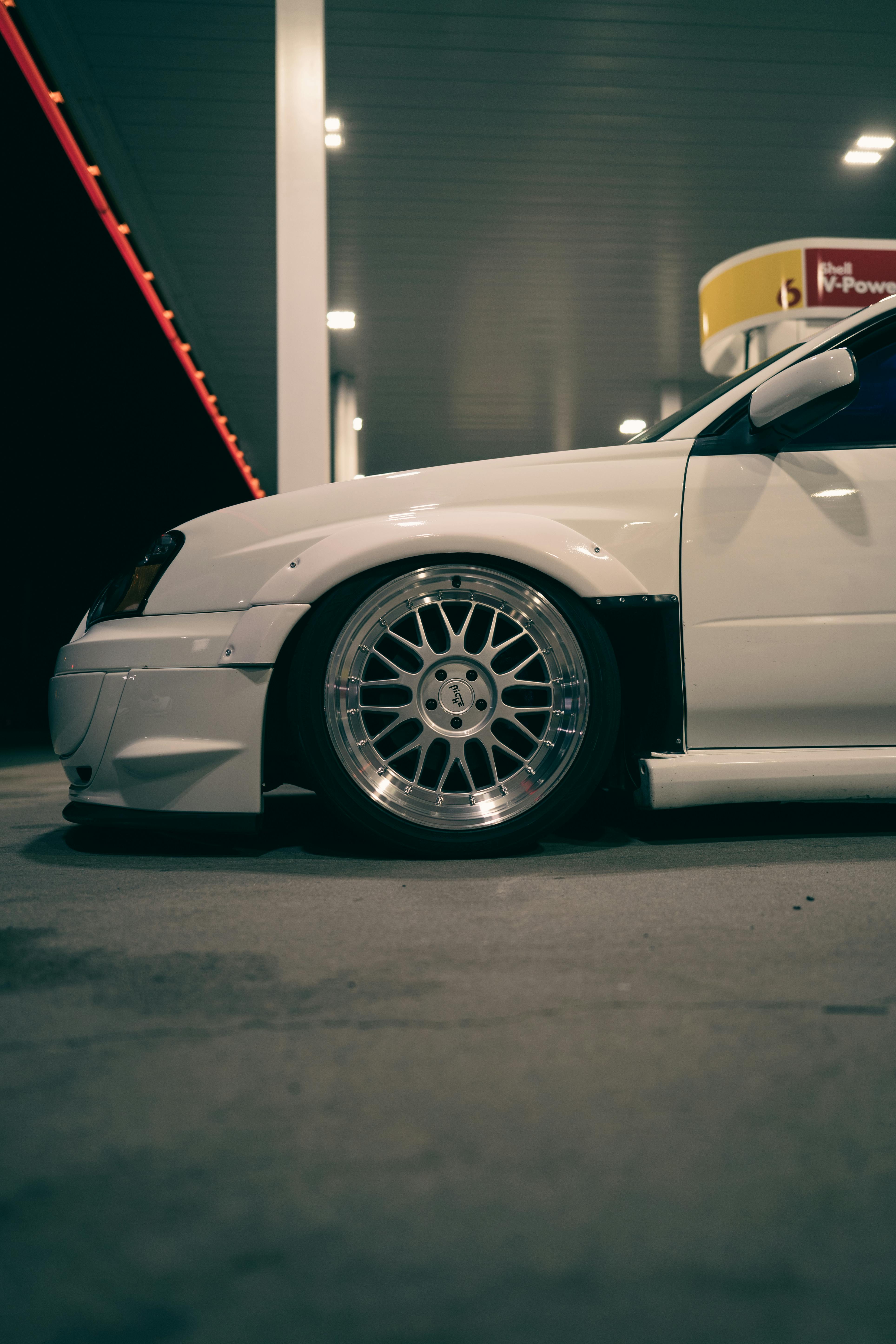 A white car with rims parked in a gas station · Free Stock Photo