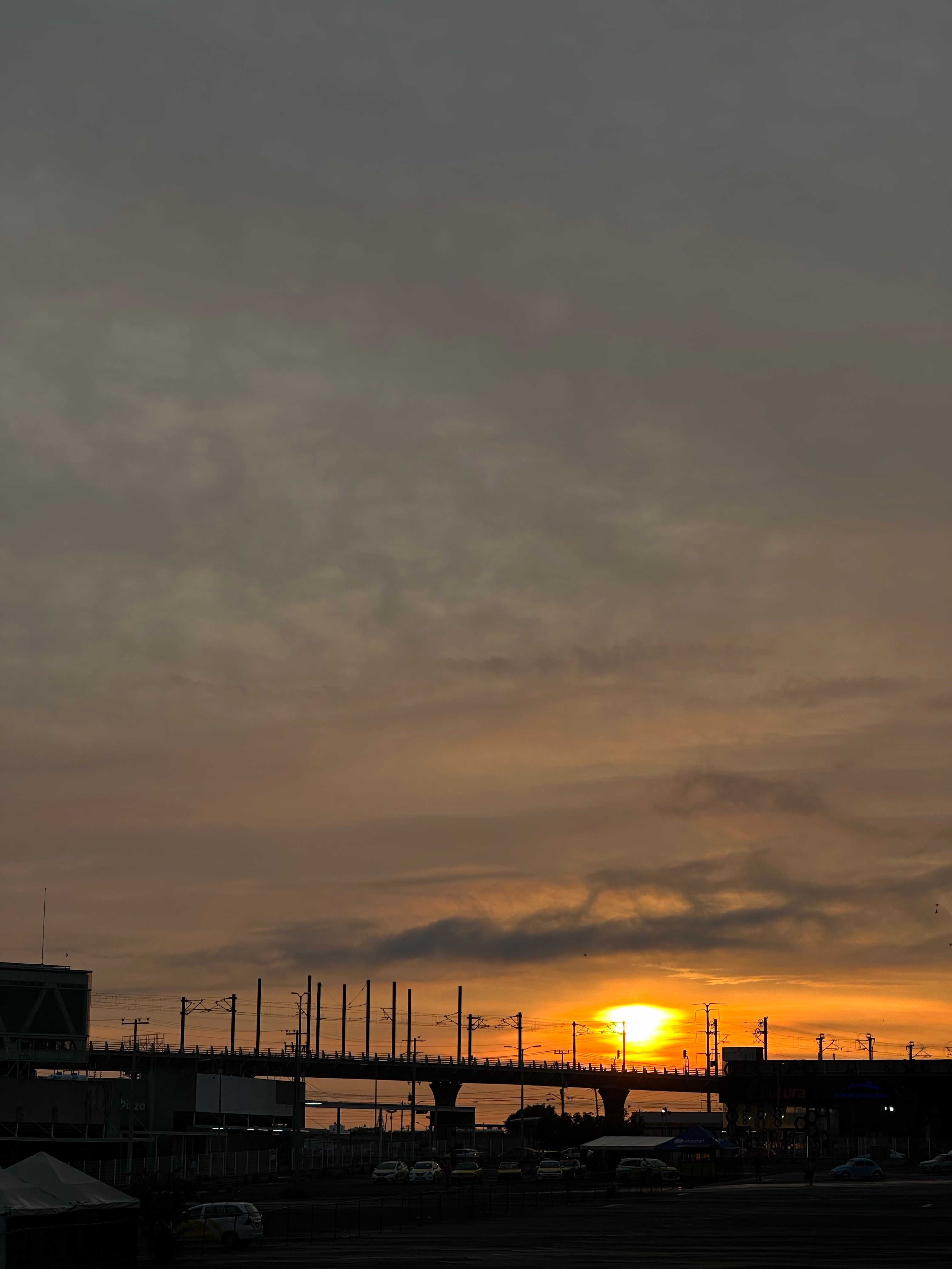 A sunset over a bridge with a plane in the sky · Free Stock Photo
