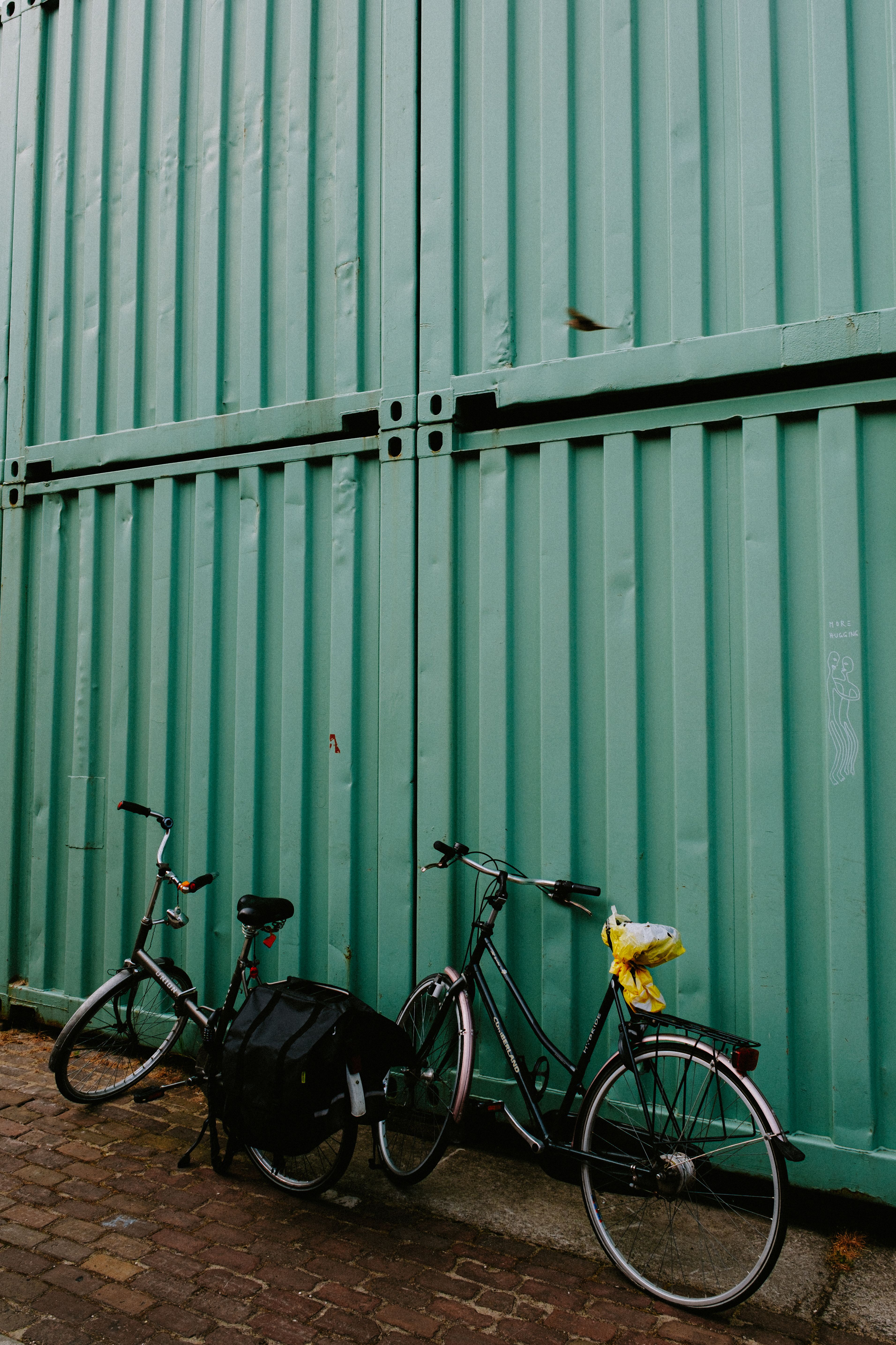 Two bicycles parked next to a green container · Free Stock Photo