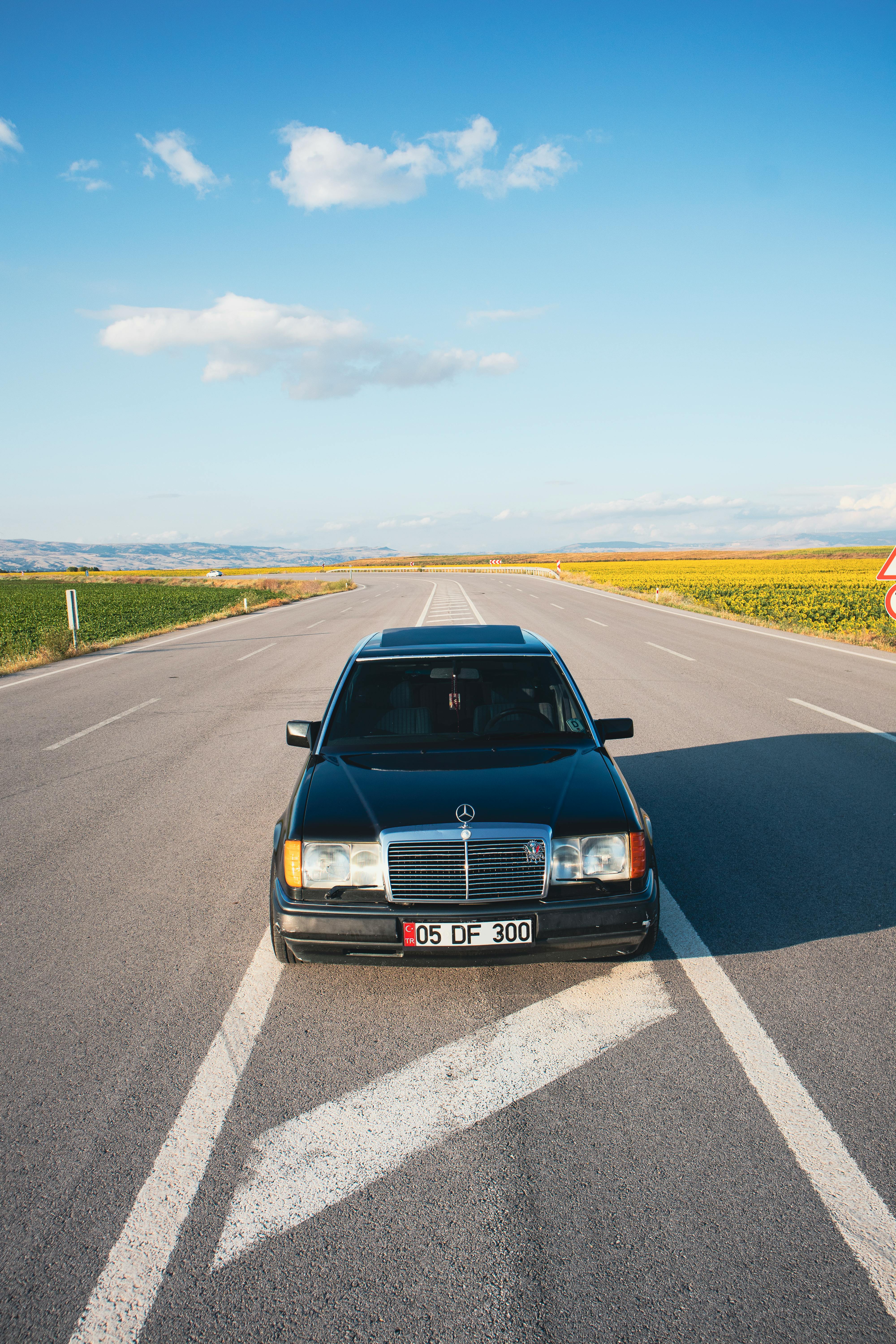 A black car driving down a road in the middle of a field · Free Stock Photo