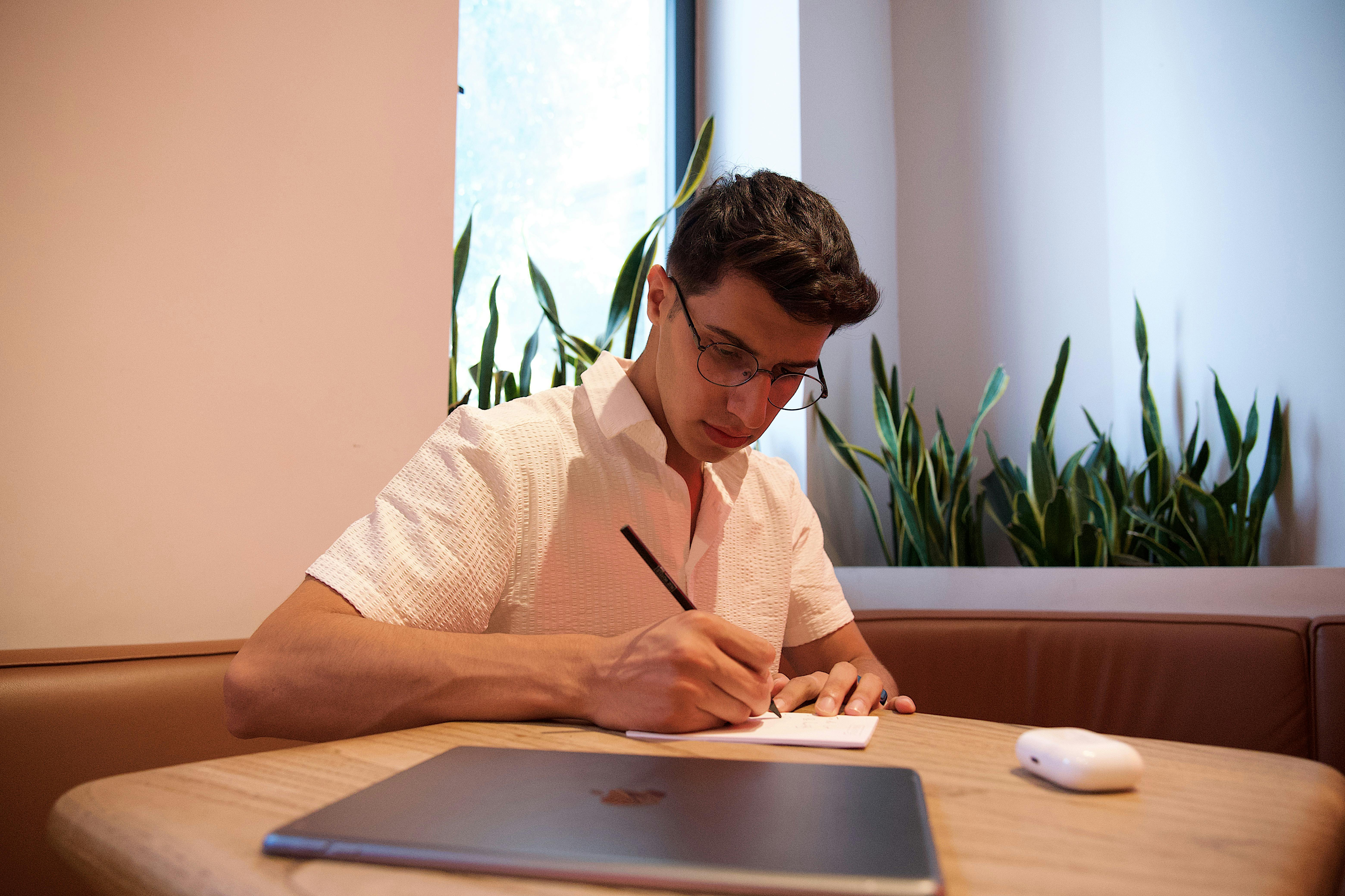 Man Sitting and Writing on Table · Free Stock Photo