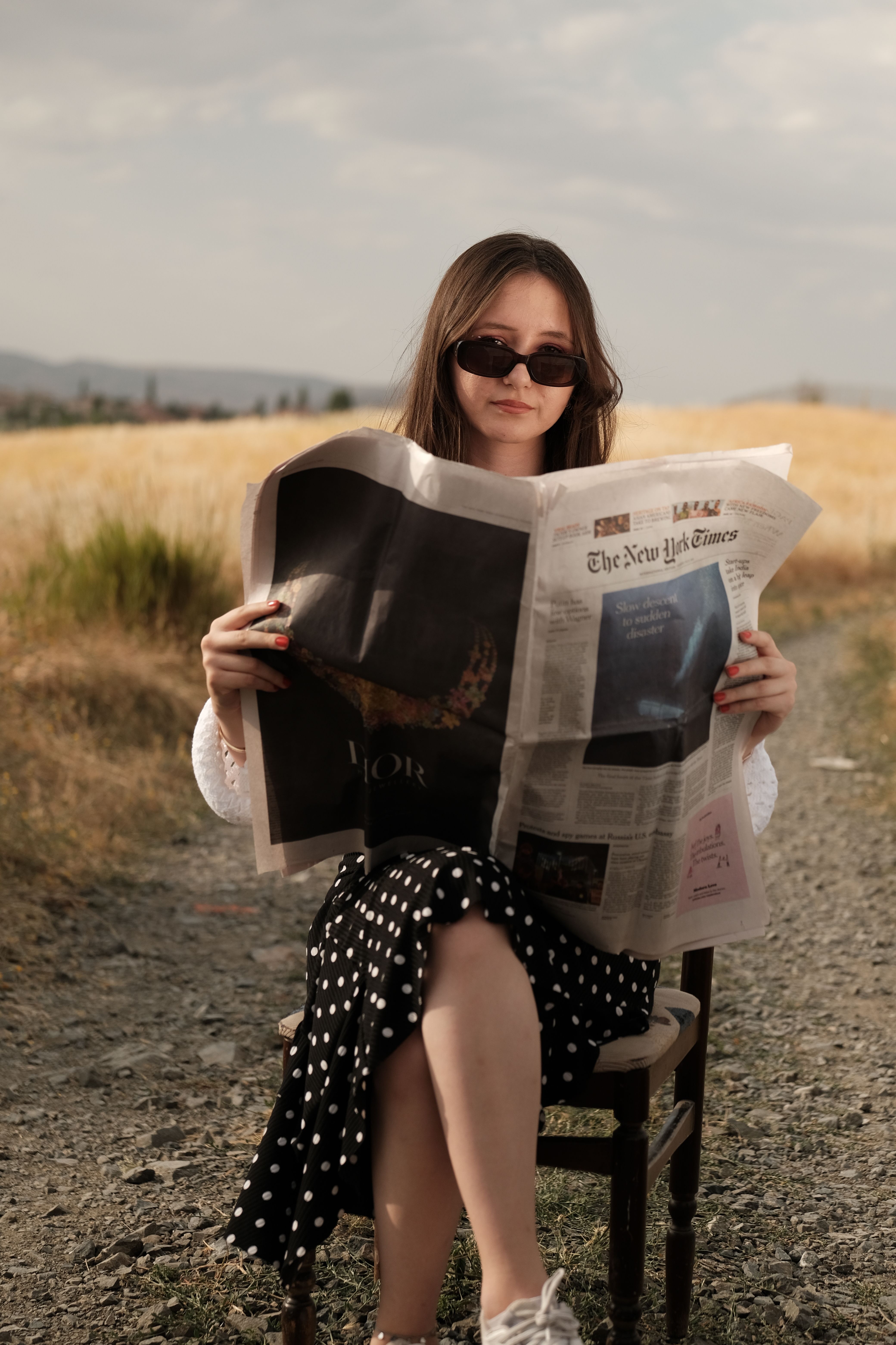 Woman in Sunglasses Sitting and Reading Newspaper on Dirt Road · Free ...