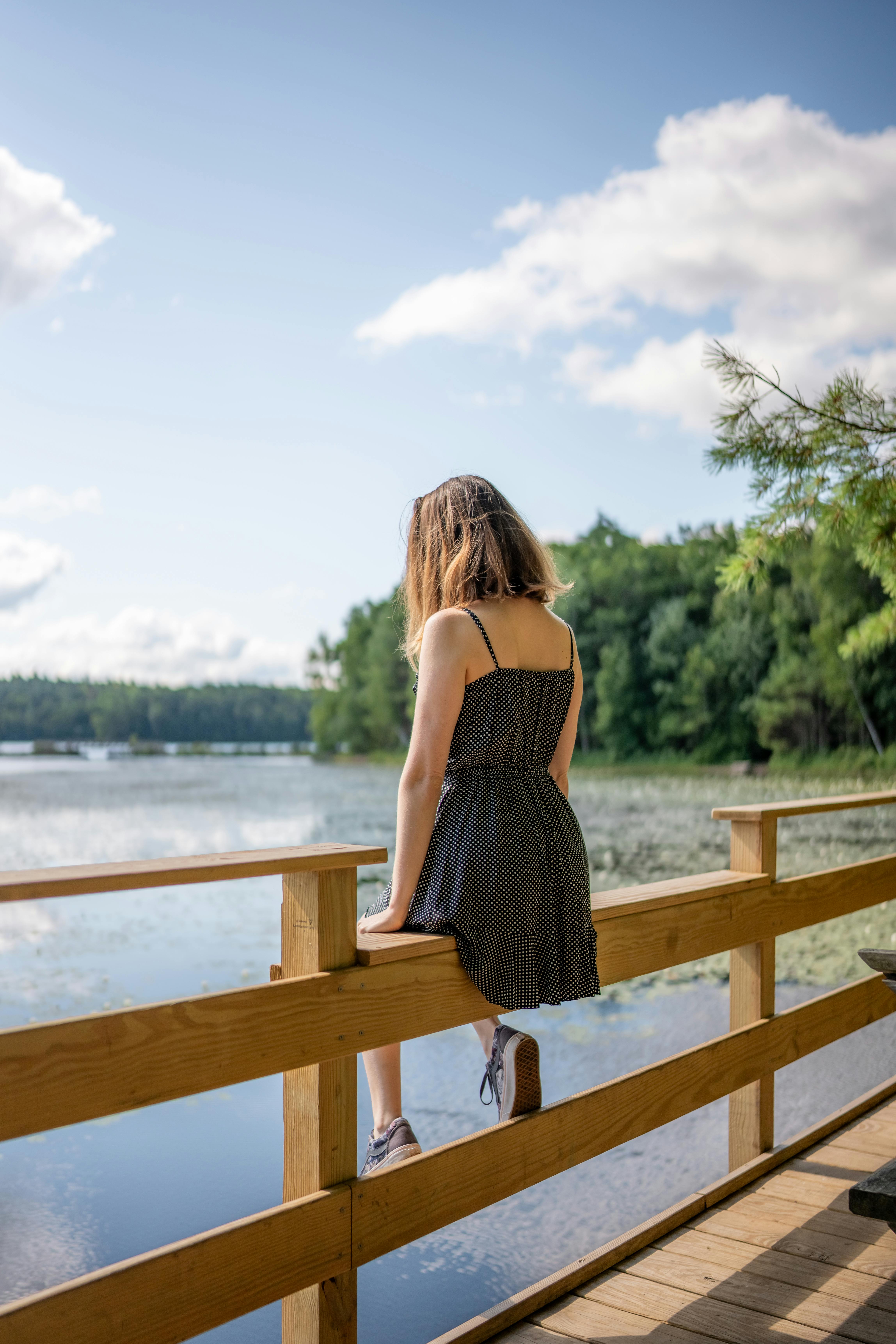 Woman in Sundress Sitting on Wooden Boardwalk Railing · Free Stock Photo