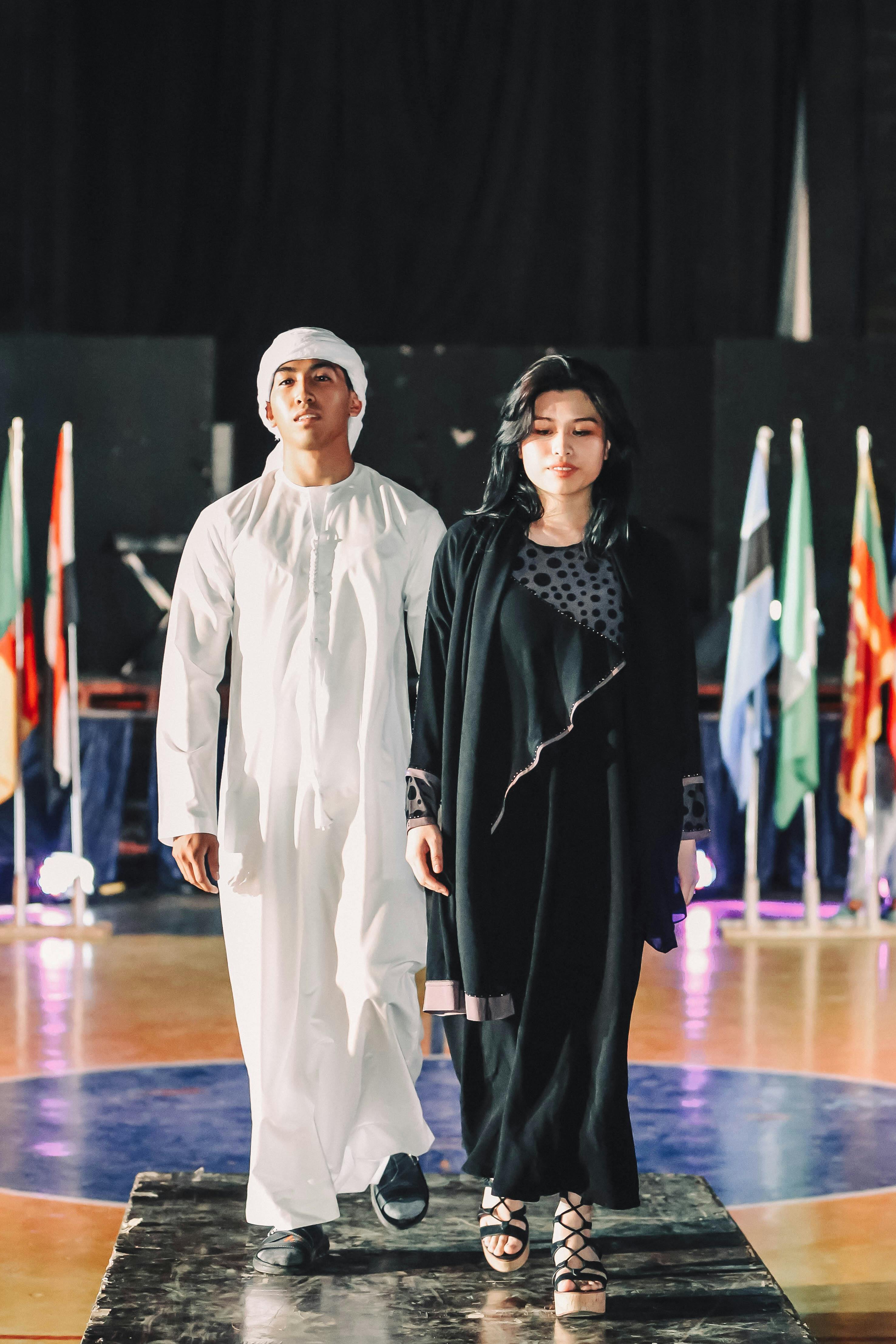 Man in White Dishdasha and Turban Next to Woman in Abayas and Scarf on the Runway · Free Stock Photo