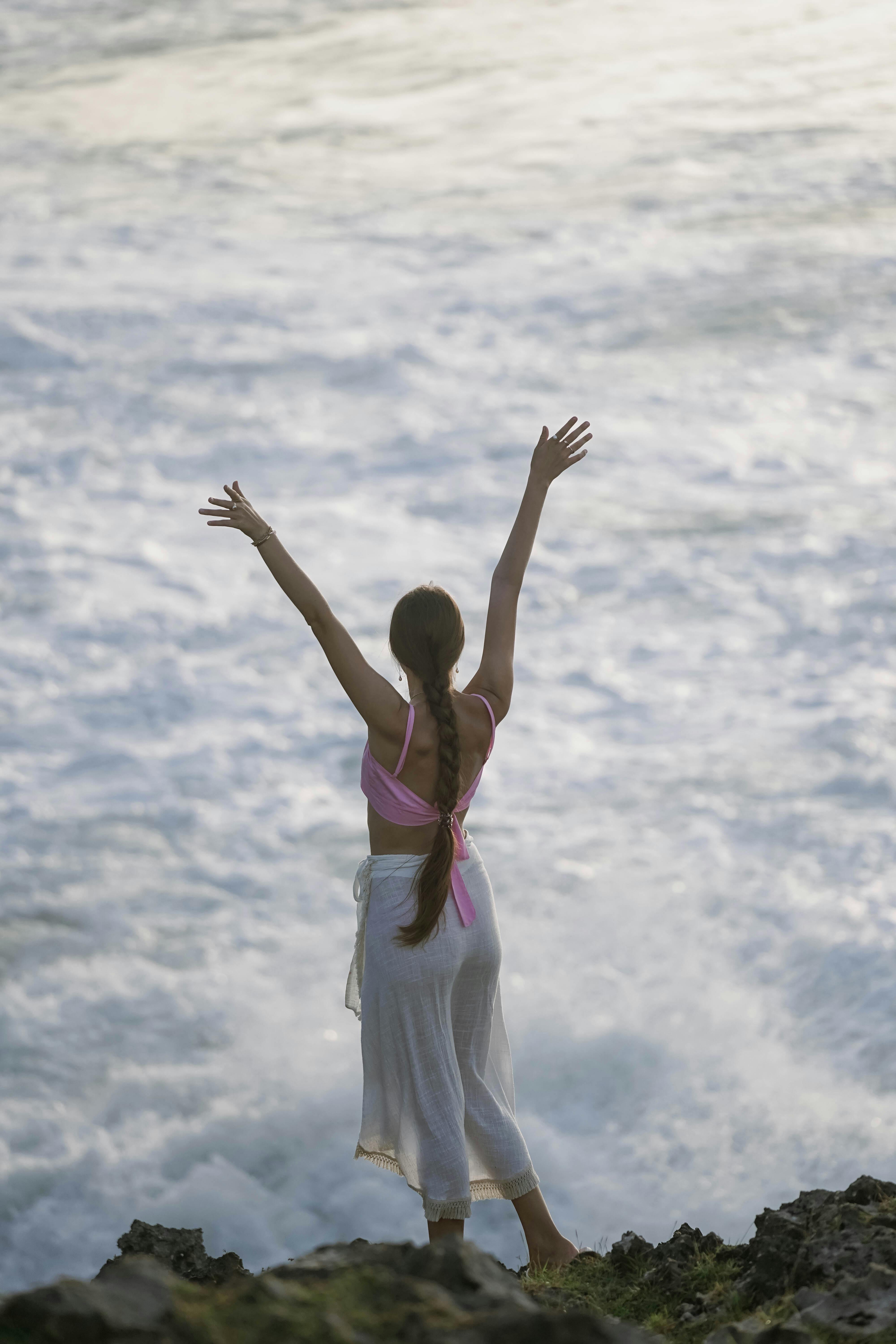 Woman Standing with Arms Raised on Sea Shore · Free Stock Photo
