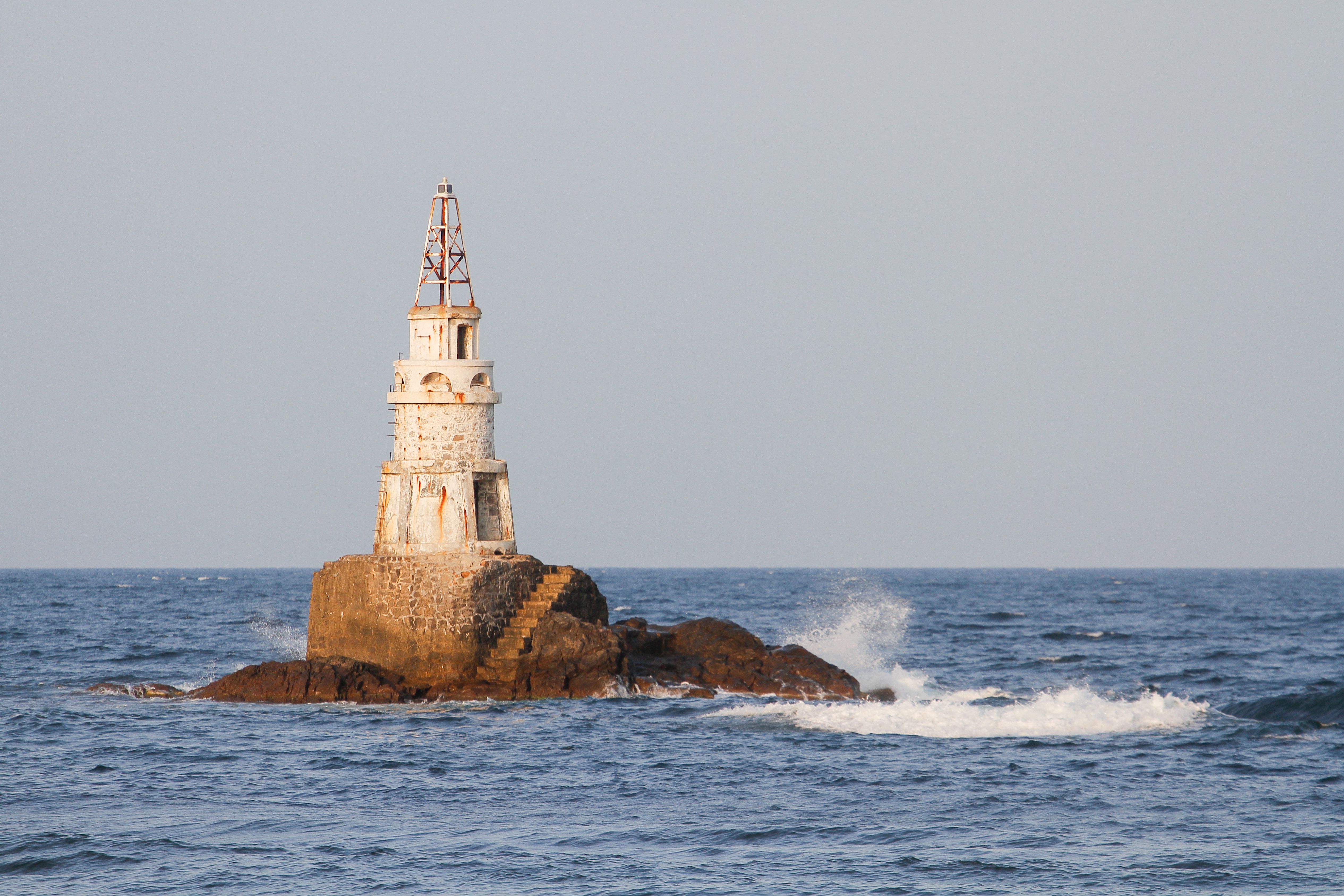 A lighthouse in the middle of the ocean with waves · Free Stock Photo