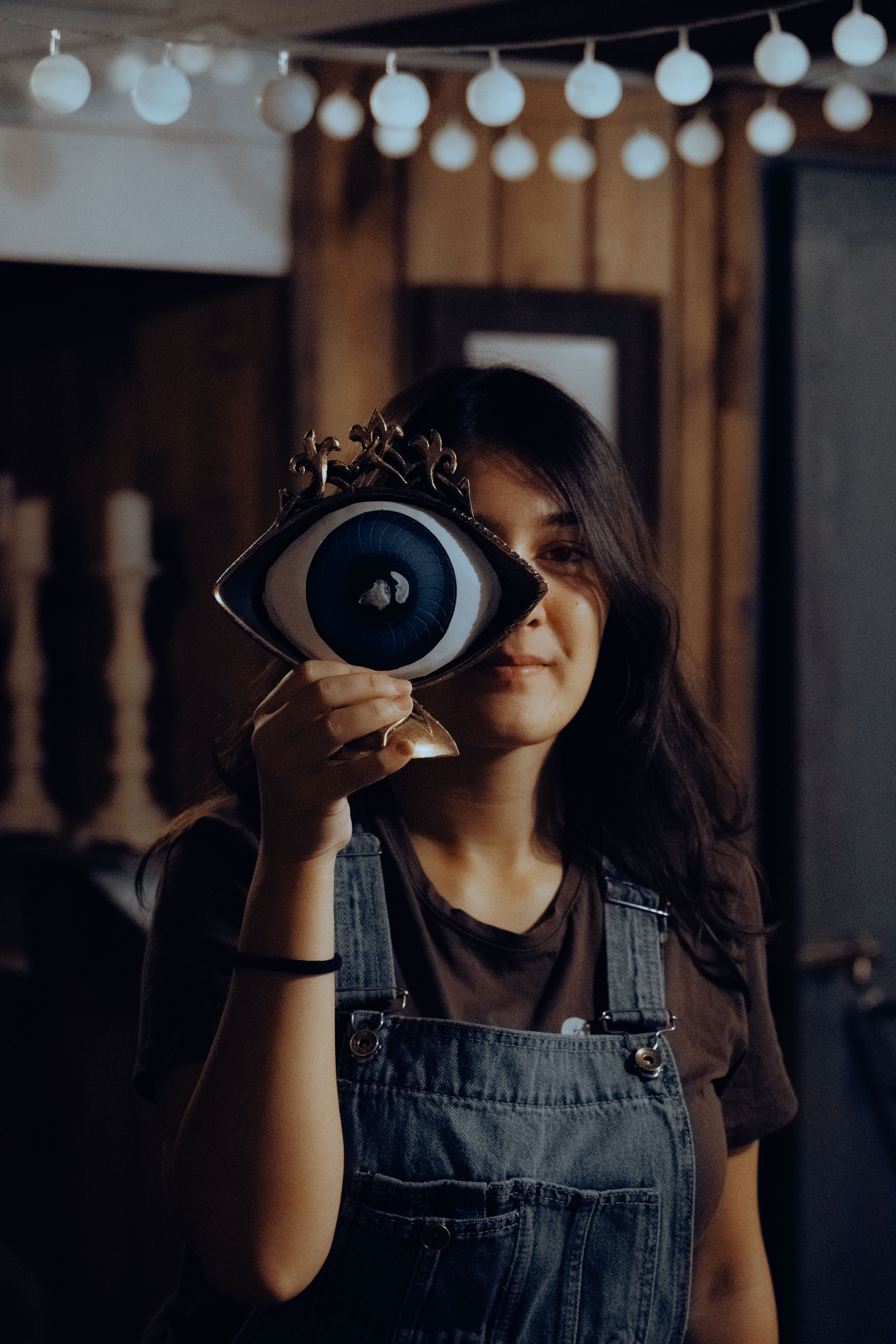 Young Woman in Overalls Holding a Figurine in the Shape of an Eye ...