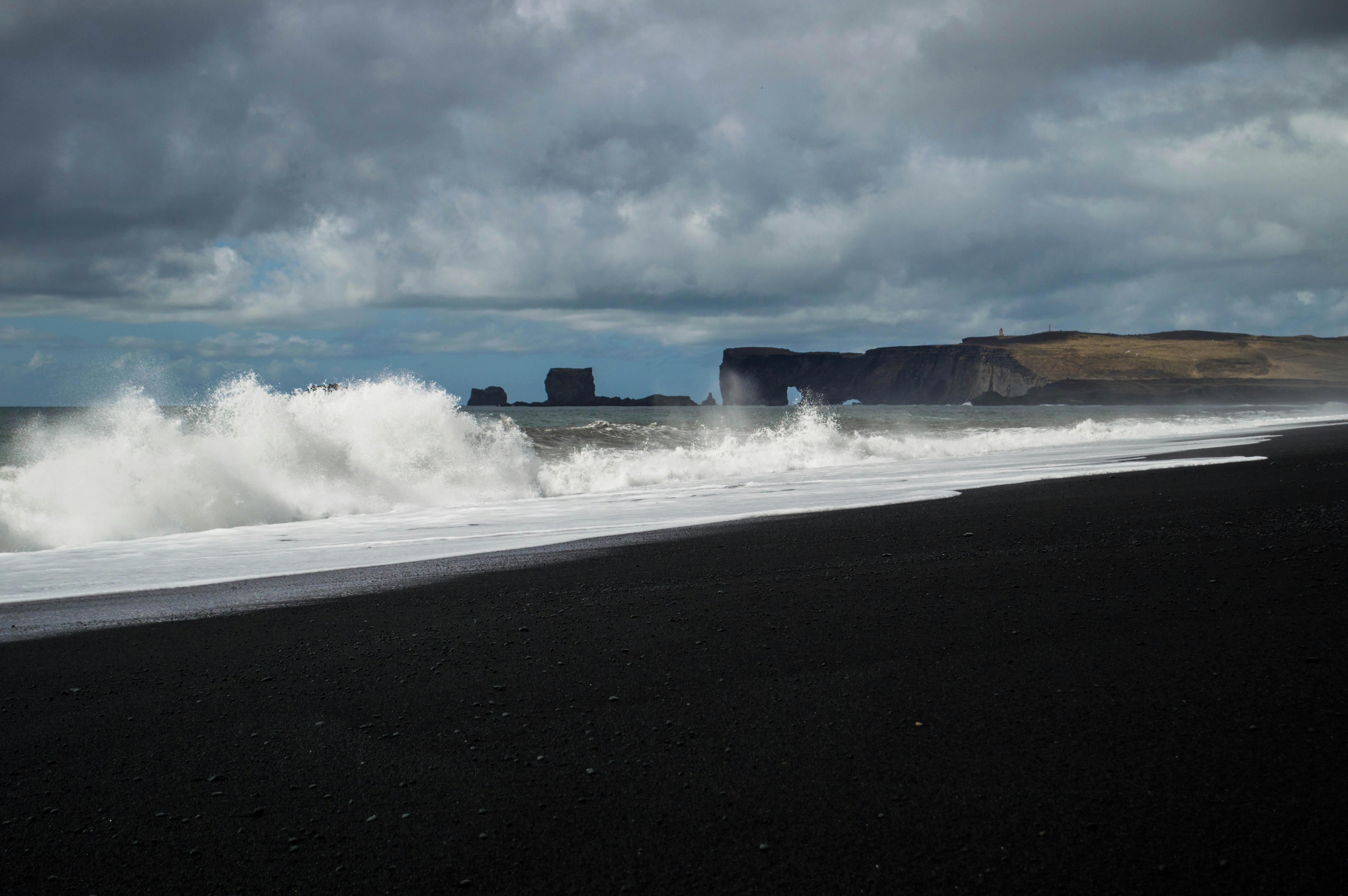 Black sand beach with waves crashing into the shore · Free Stock Photo