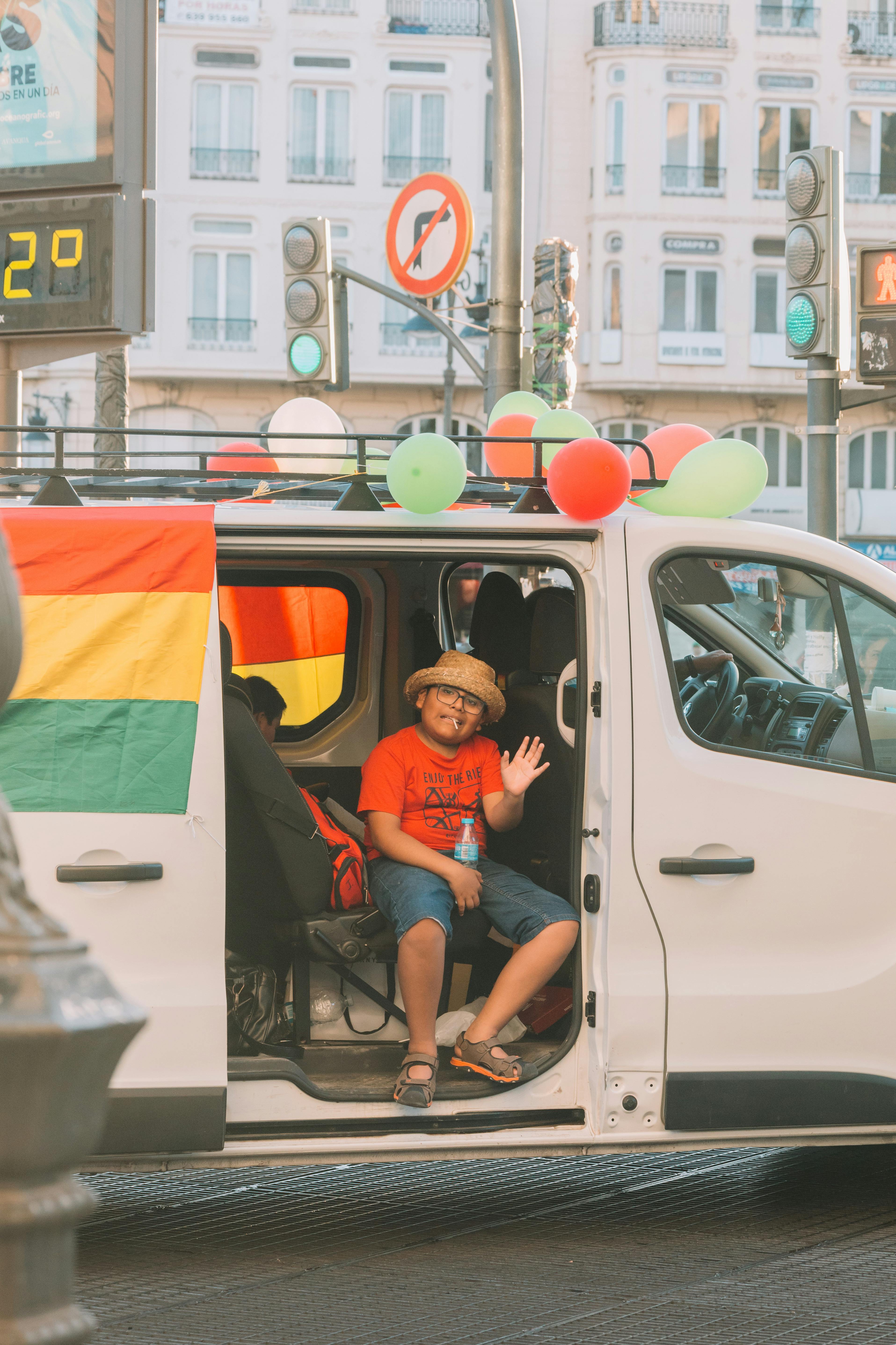 A Boy Sitting on the Back of the Van and Waving · Free Stock Photo