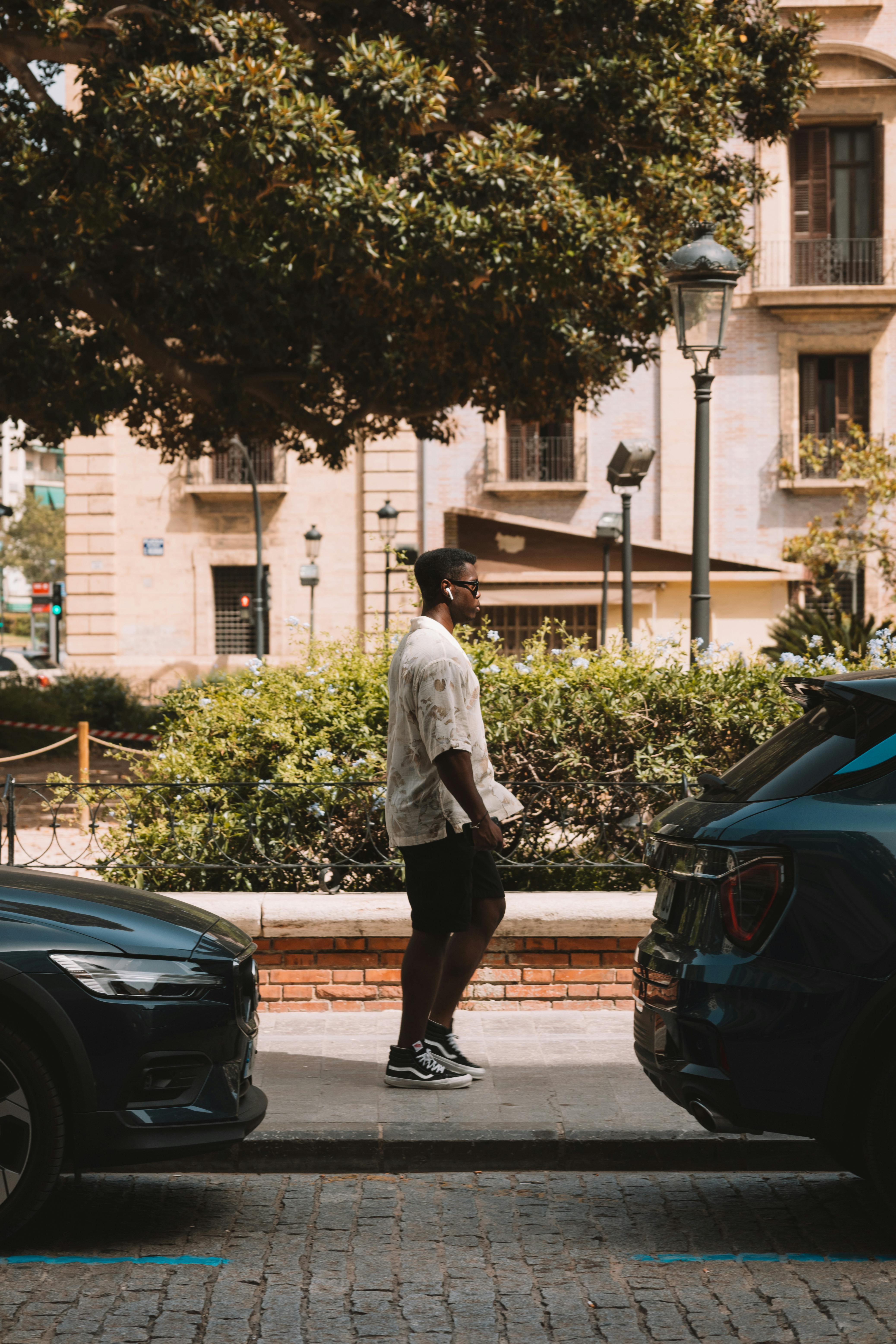 Man Standing between Cars on Sidewalk · Free Stock Photo