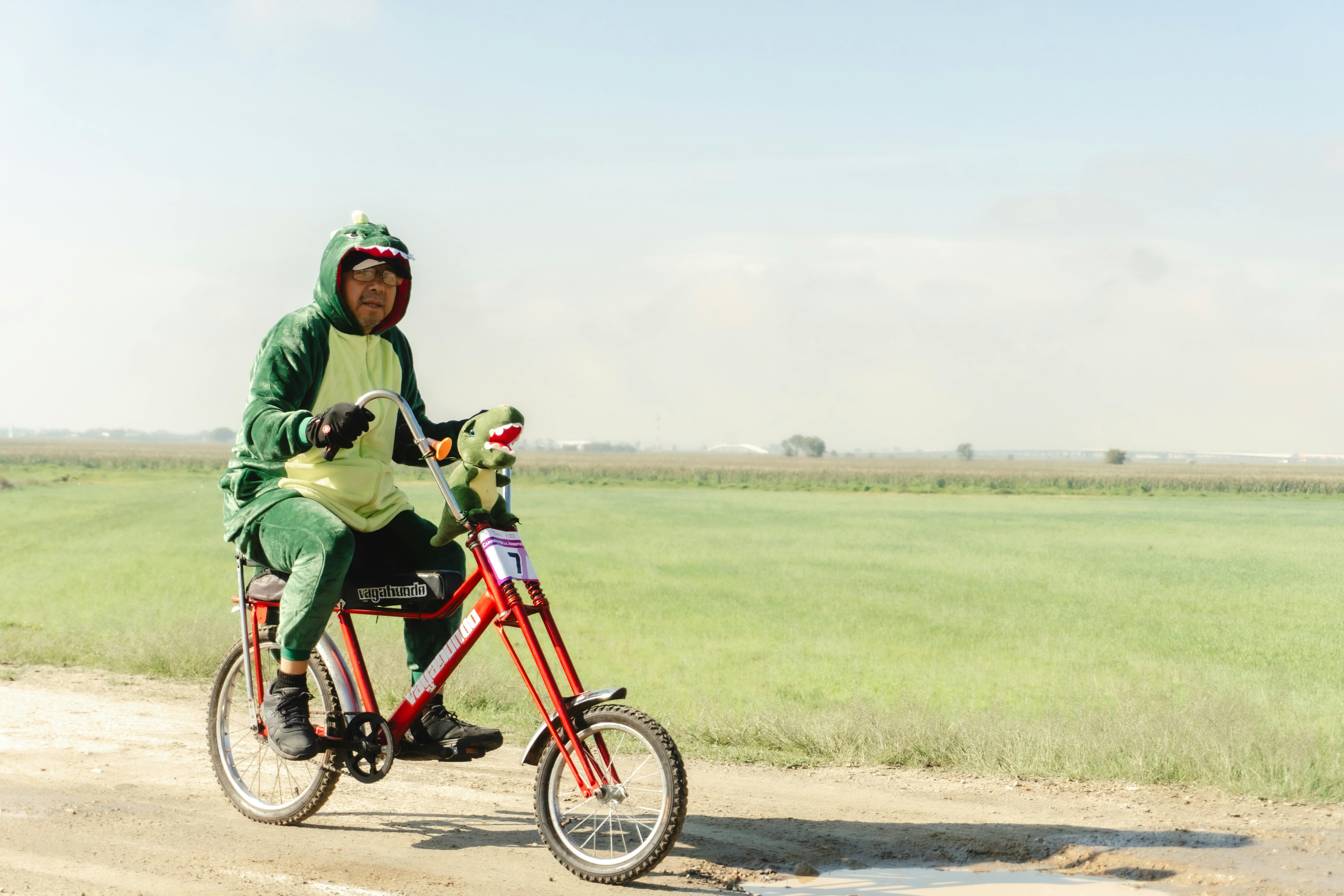 Man in Dinosaur Costume Riding Bike in Countryside · Free Stock Photo