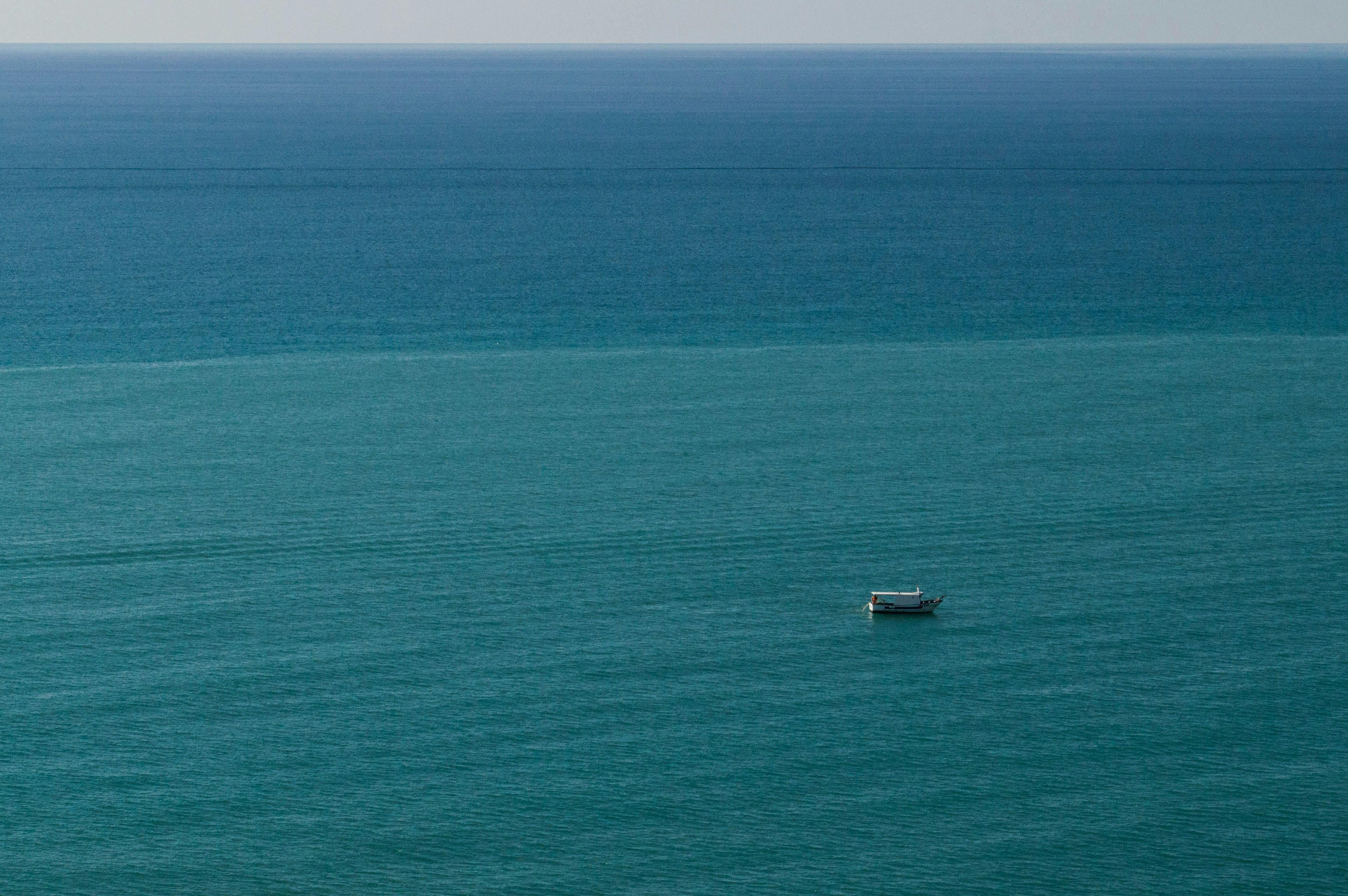 A boat is floating in the ocean near a cliff · Free Stock Photo