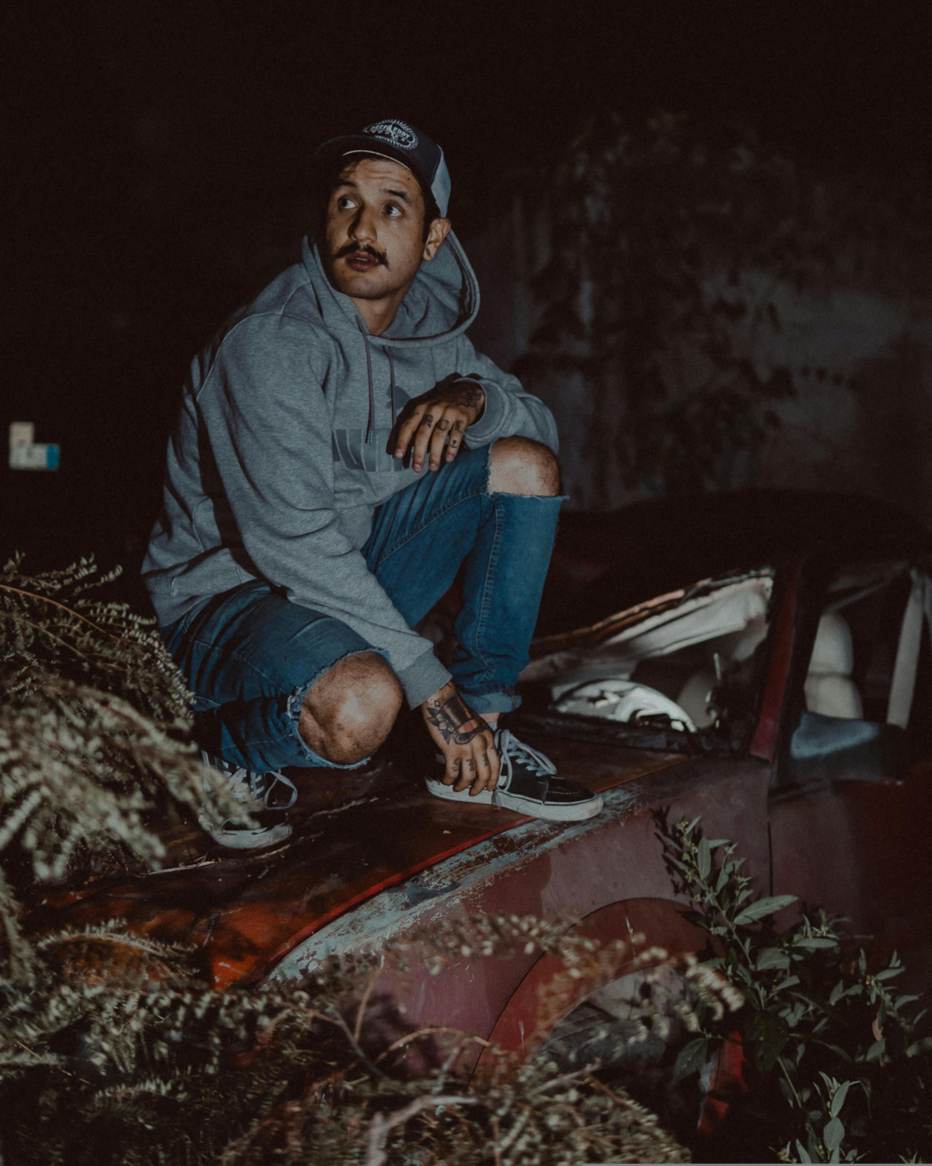 A Man in a Hoodie Crouching on the Hood of an Abandoned Car · Free ...