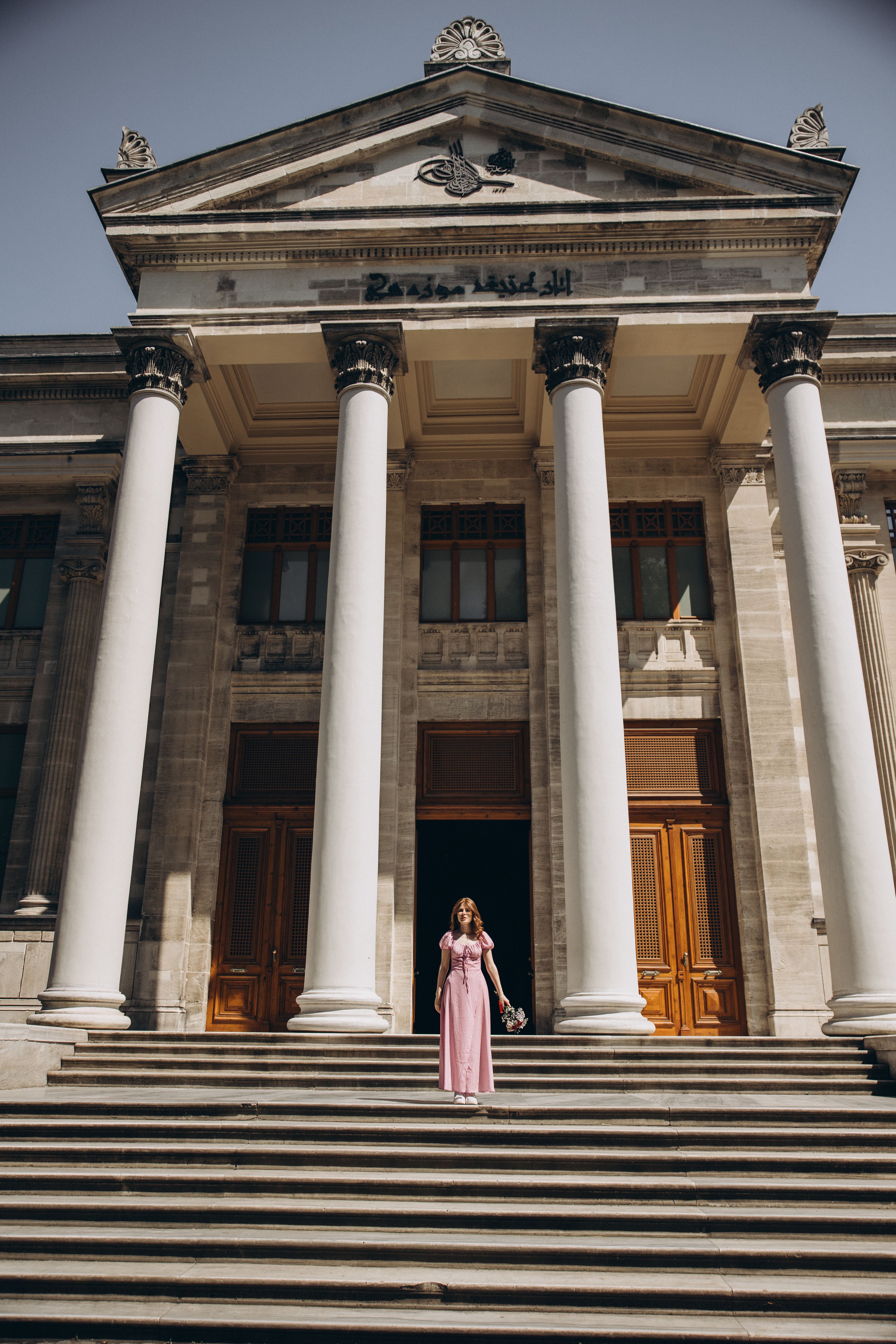 A woman in a pink dress stands on the steps of a building · Free Stock ...