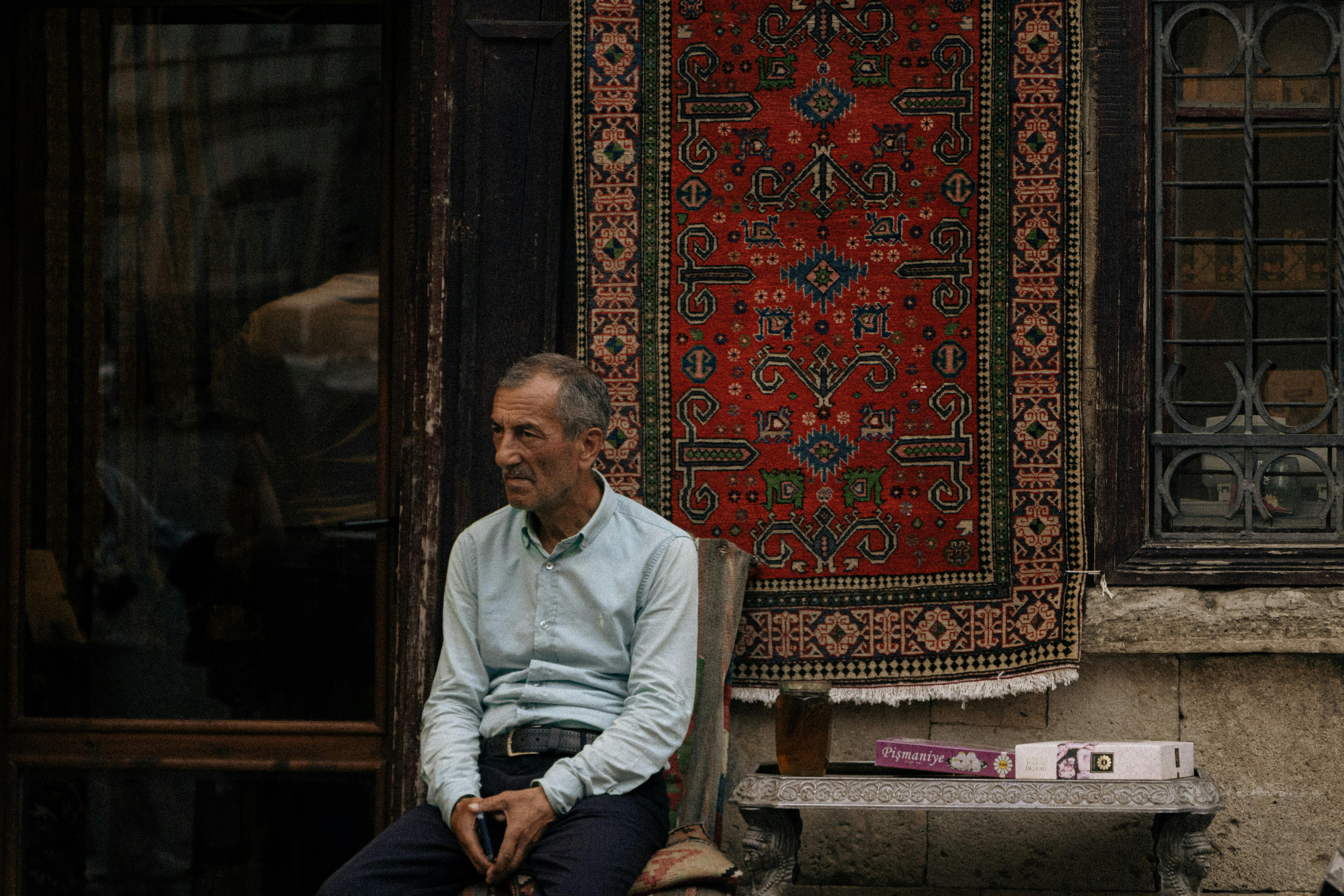 Man Sitting on Street by Ornate Carpet · Free Stock Photo