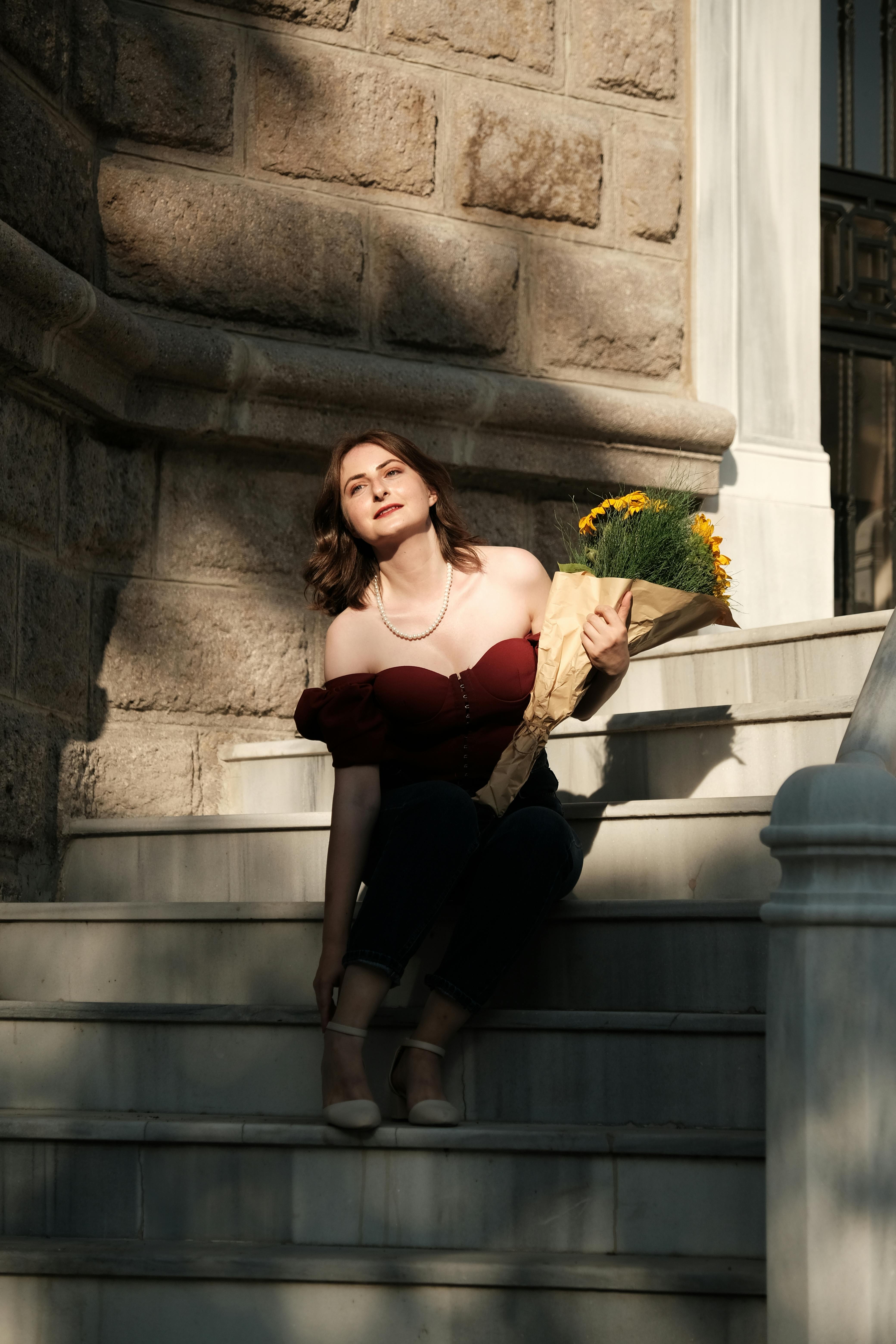 Woman in White Shirt Sitting on a Wall with Fedora Hat and Pink Flower ...