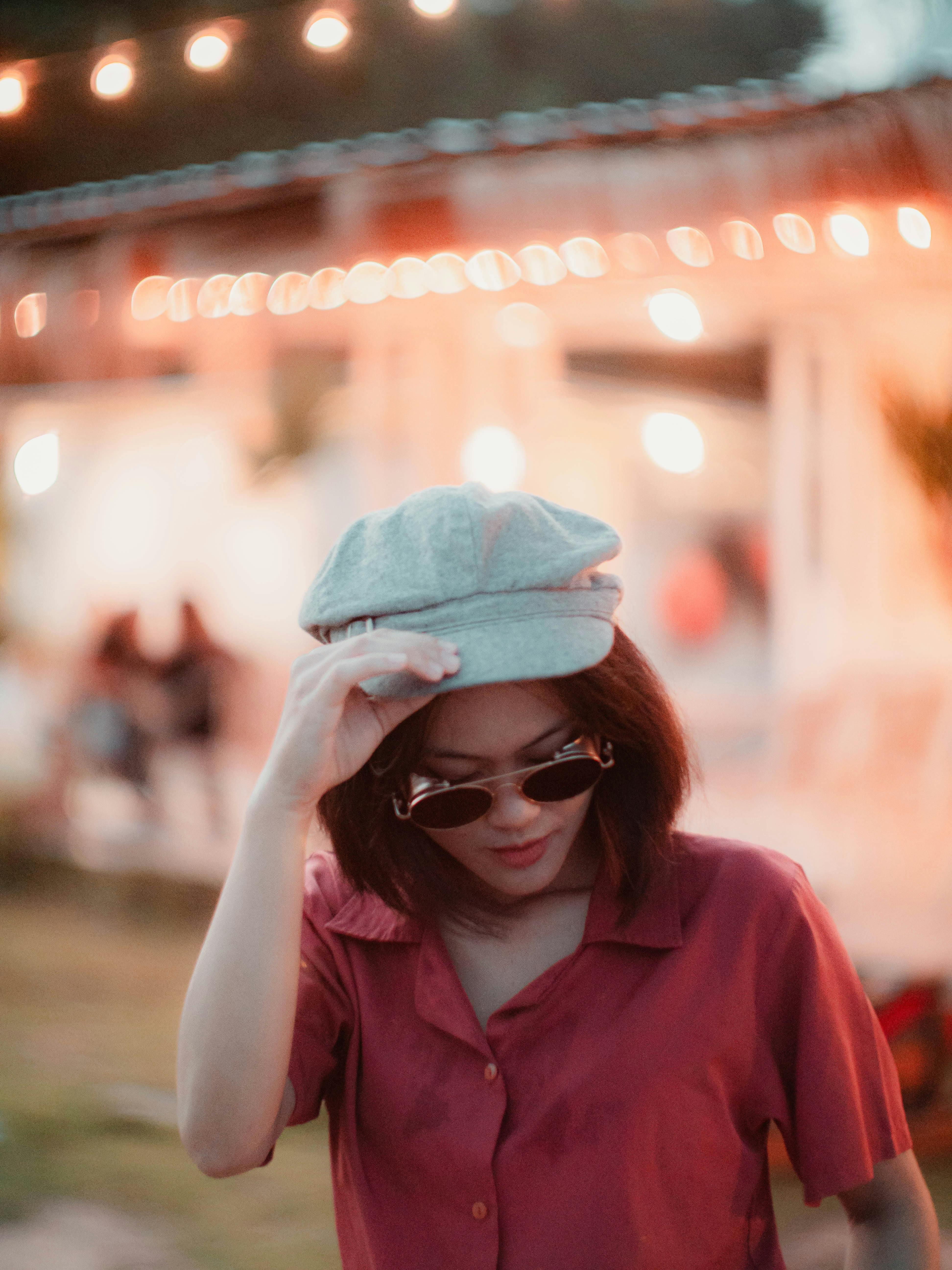 Woman in Red Shirt Posing with Hand on Cap · Free Stock Photo
